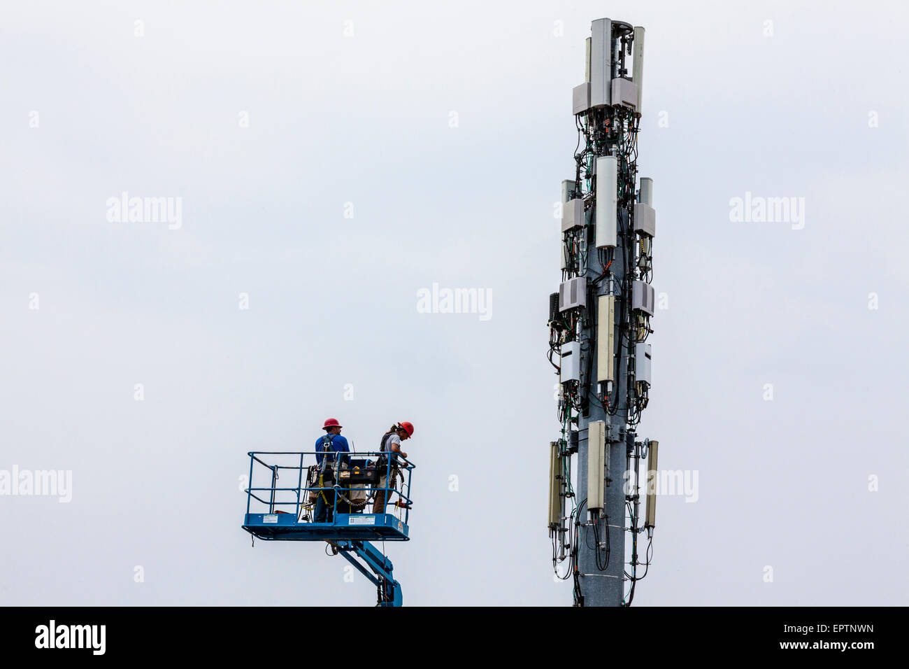 Two men working from a lift bucket on a mobile or cell phone tower in ...