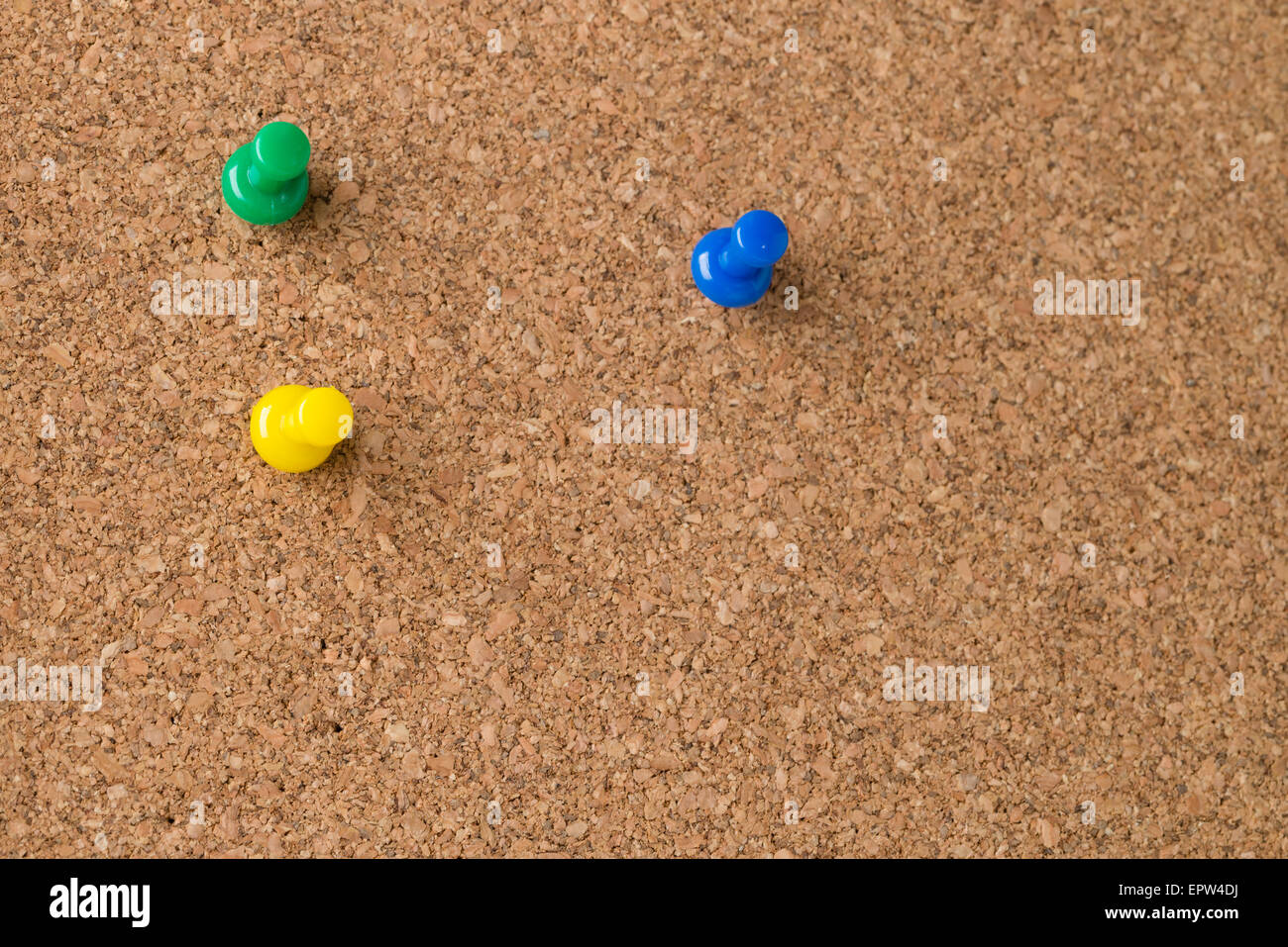 A blue, green and yellow thumb tack on a cork board Stock Photo - Alamy