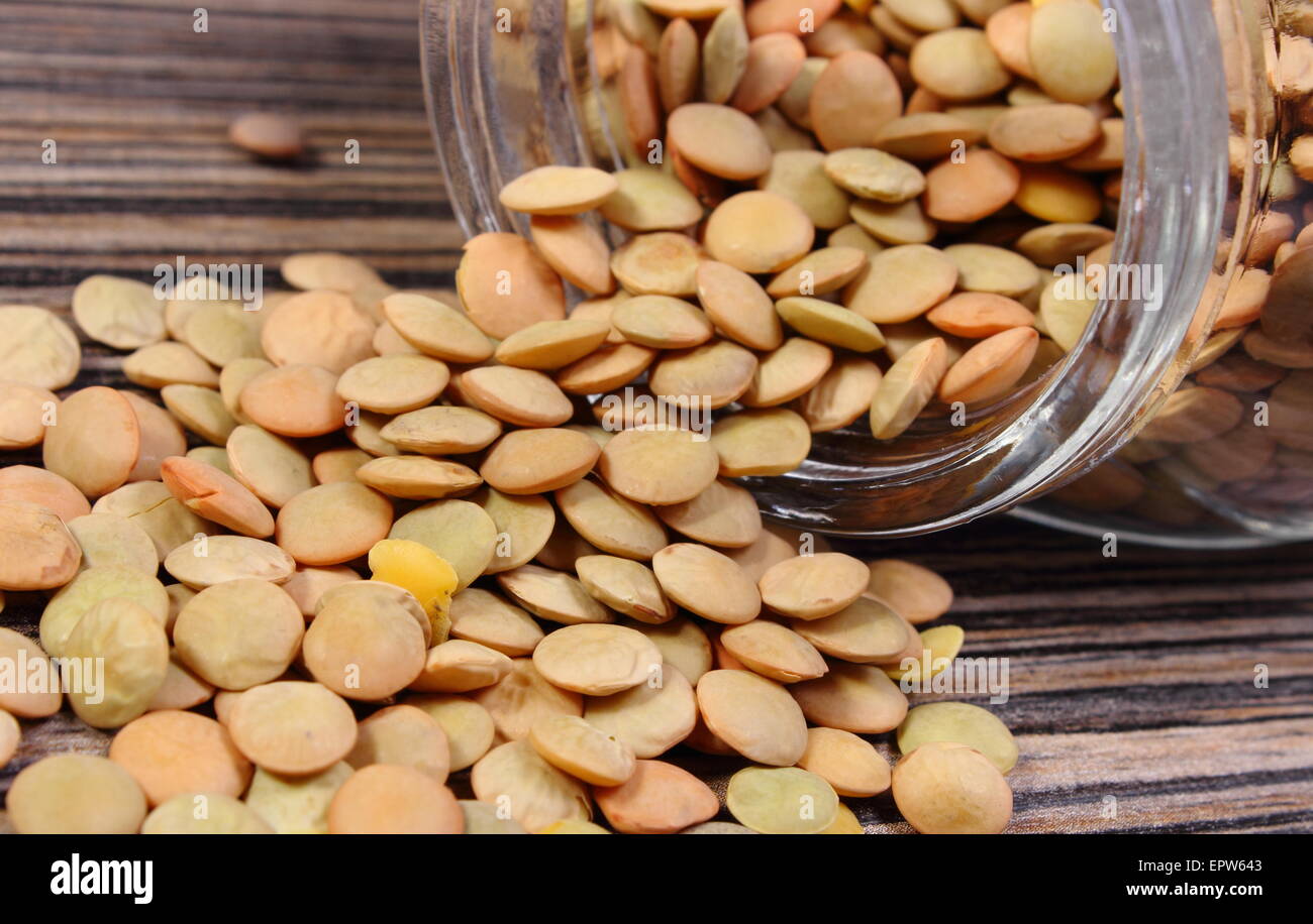 Heap of raw green lentil spilling out of glass jar on wooden background ...