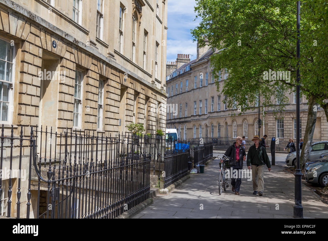 Two men walk with a bicycle along pavement next to georgian terrace ...