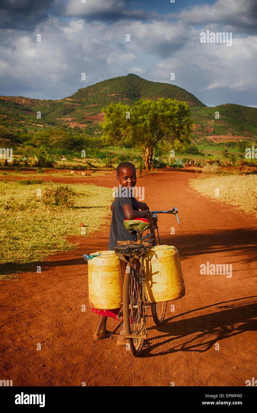 Litlle African girl carry water cannisters on the back of a bicycle, in ...