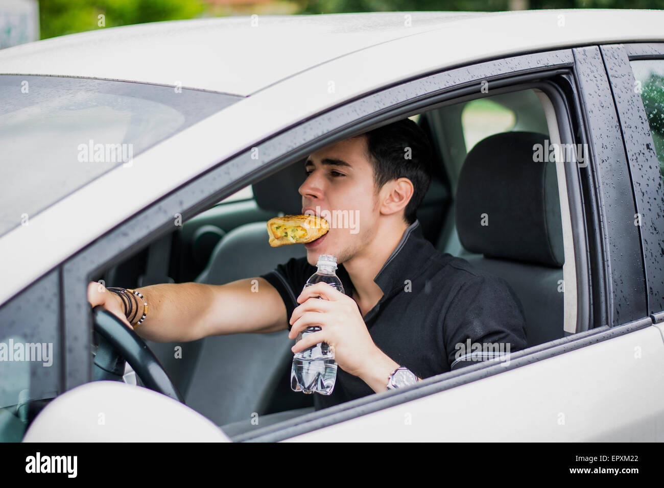Young handsome man driving his car while eating food in the traffic ...