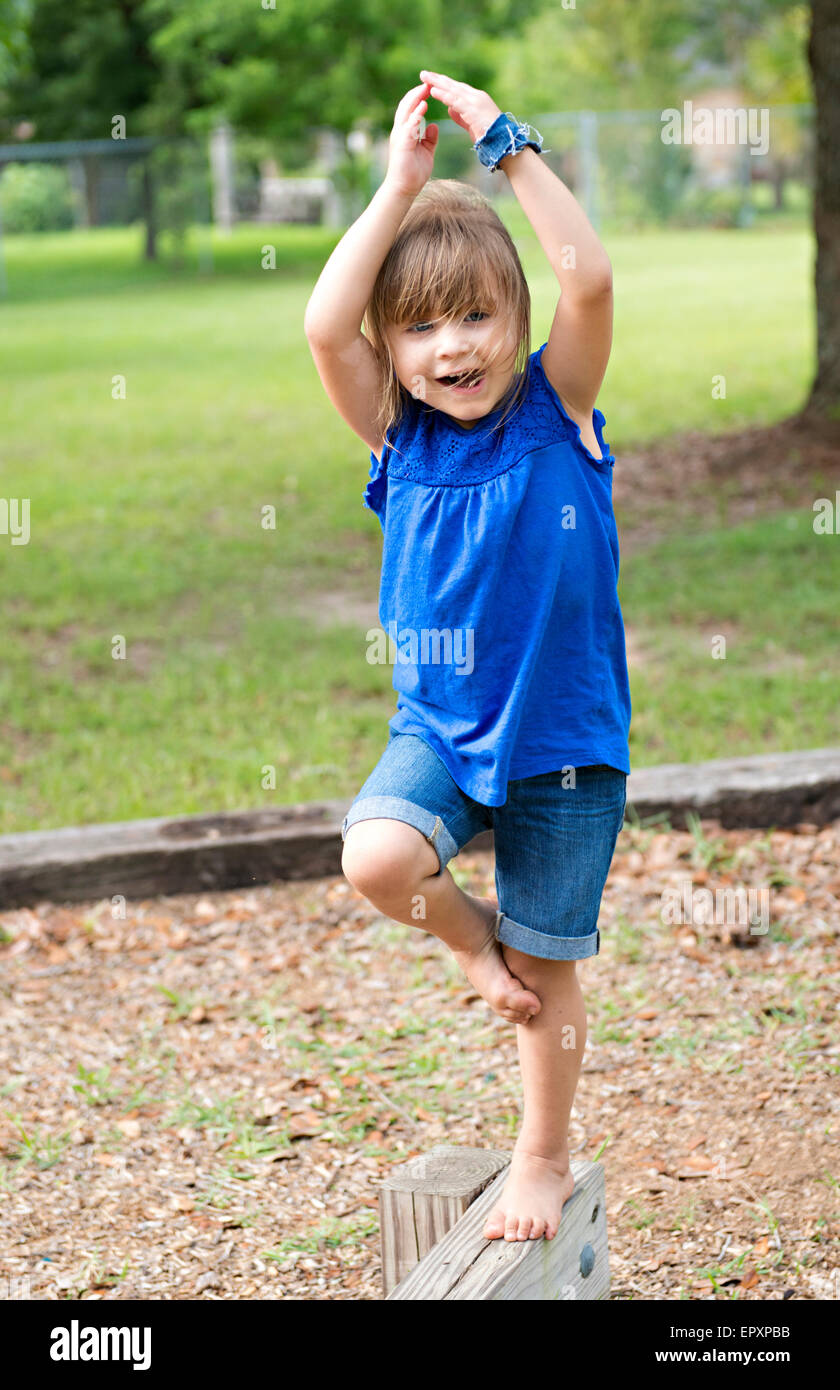 Child walking on an outdoor wooden balance beam with a ballerina pose ...