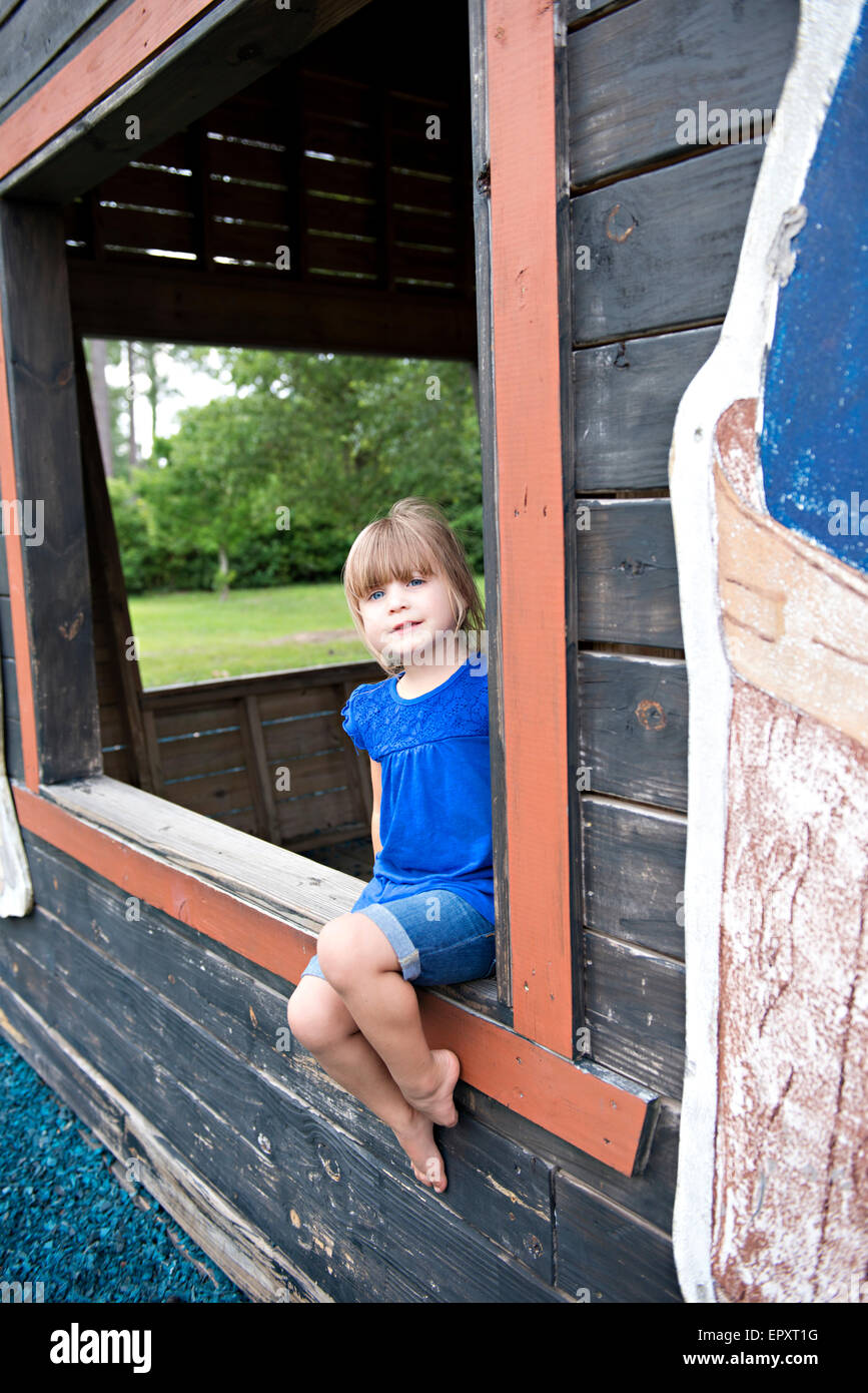 Young girl poses for a portrait while sitting in a window of an outdoor ...
