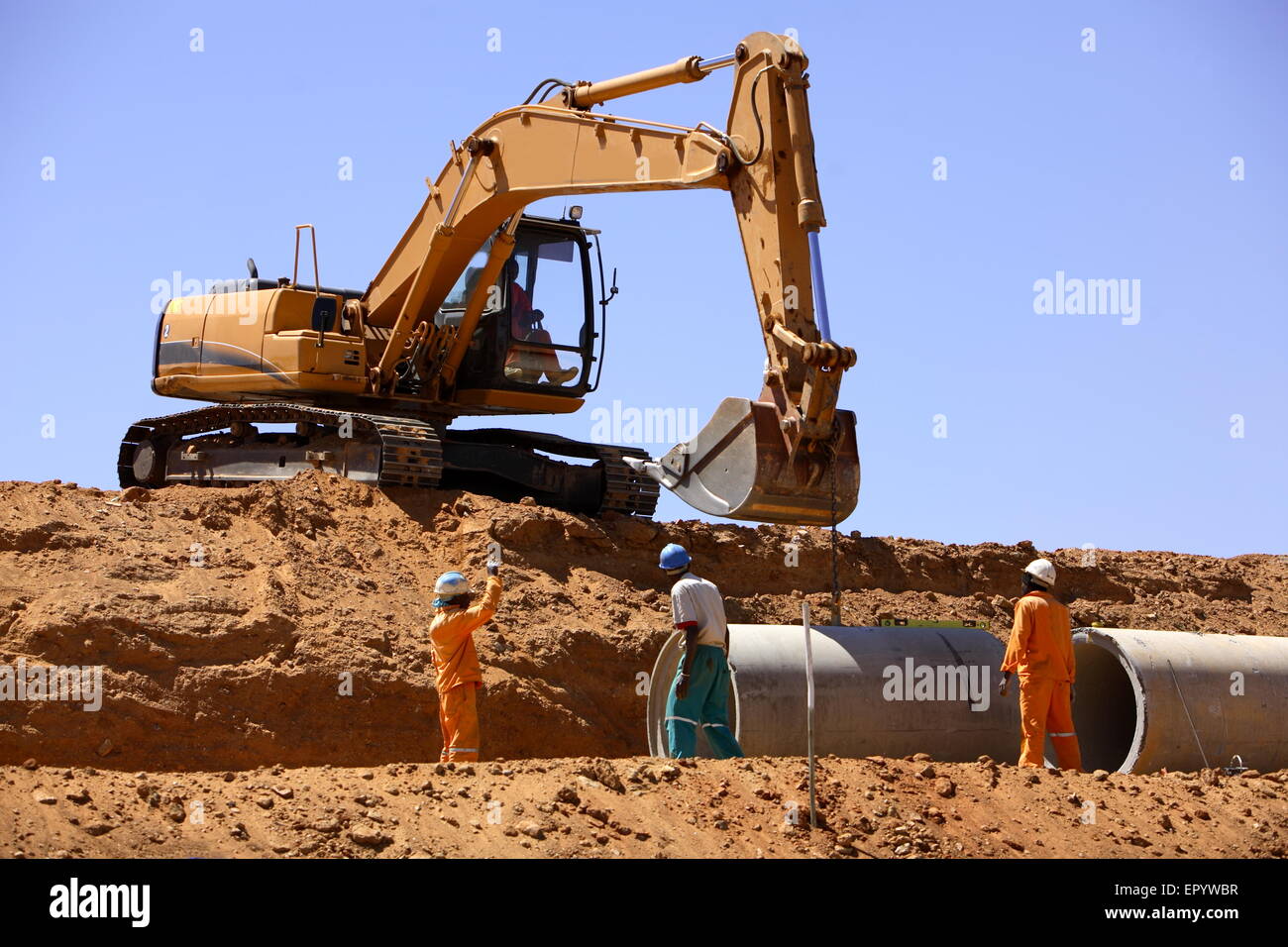 Excavator assisting workers laying concrete pipes on a construction ...