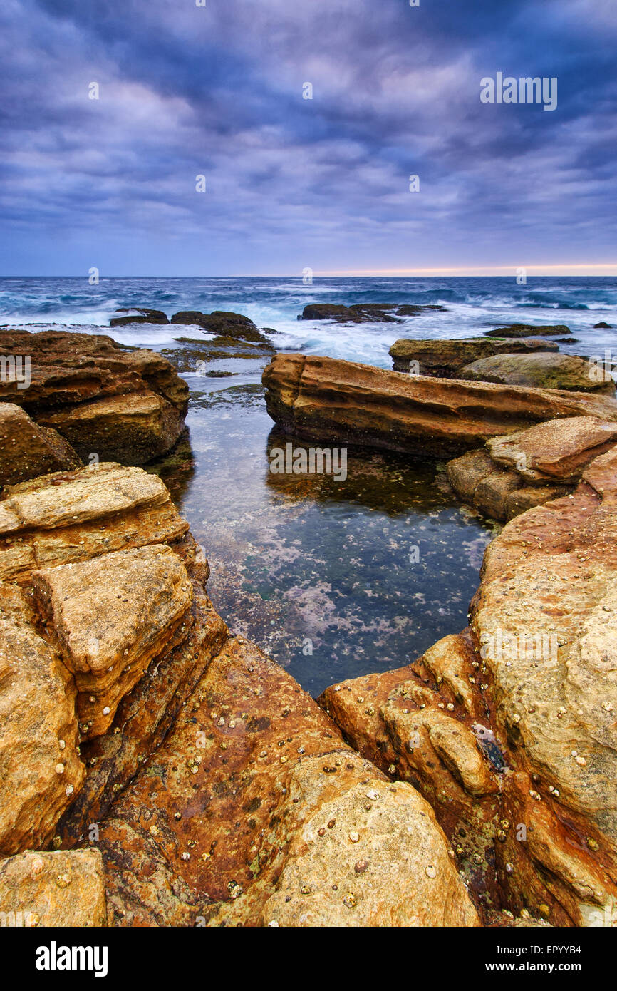 Sunrise seascape with orange rocks and ocean pools and sea shells with ...