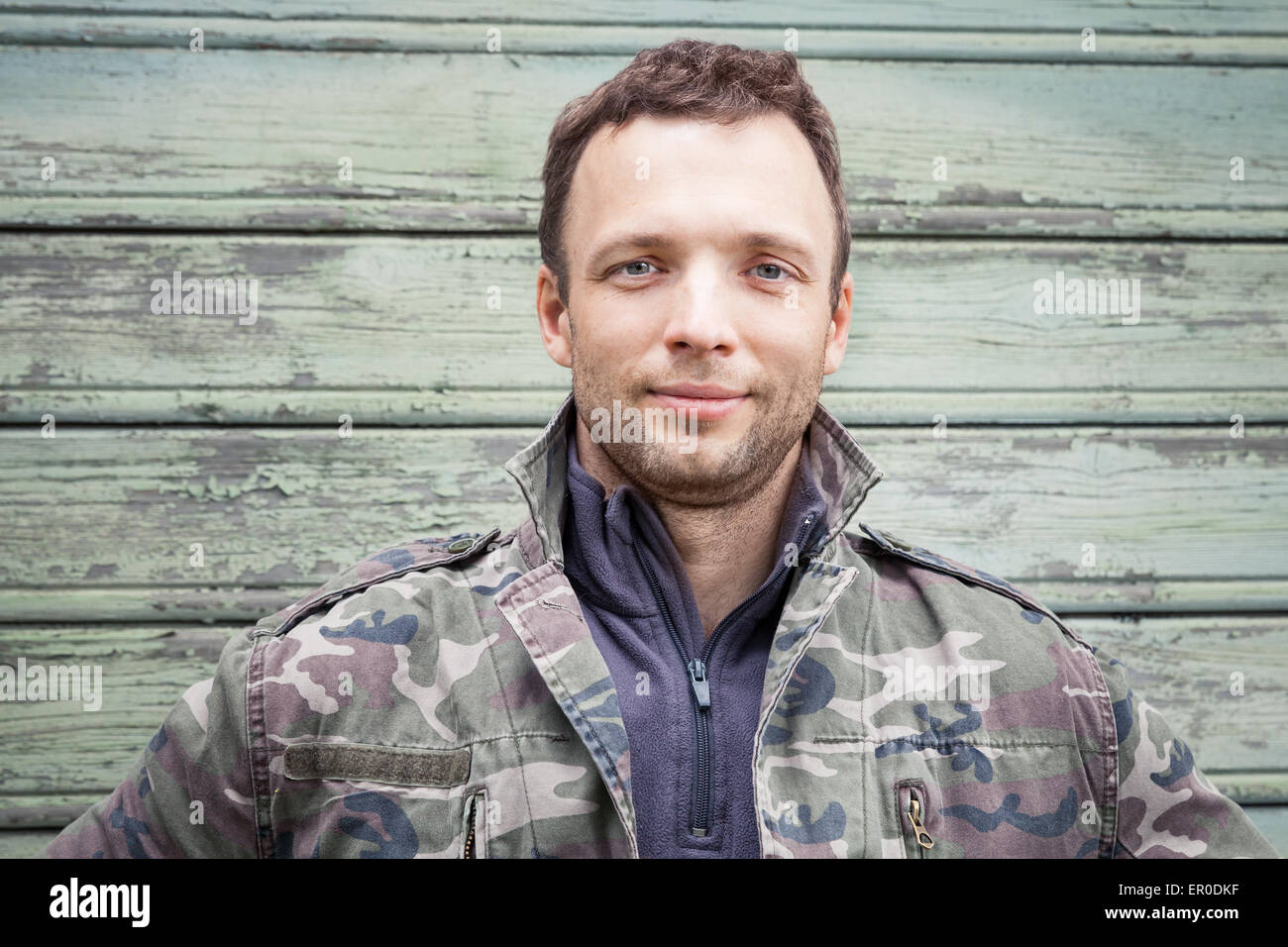 Young Caucasian man in camouflage. Outdoor portrait over green rural ...
