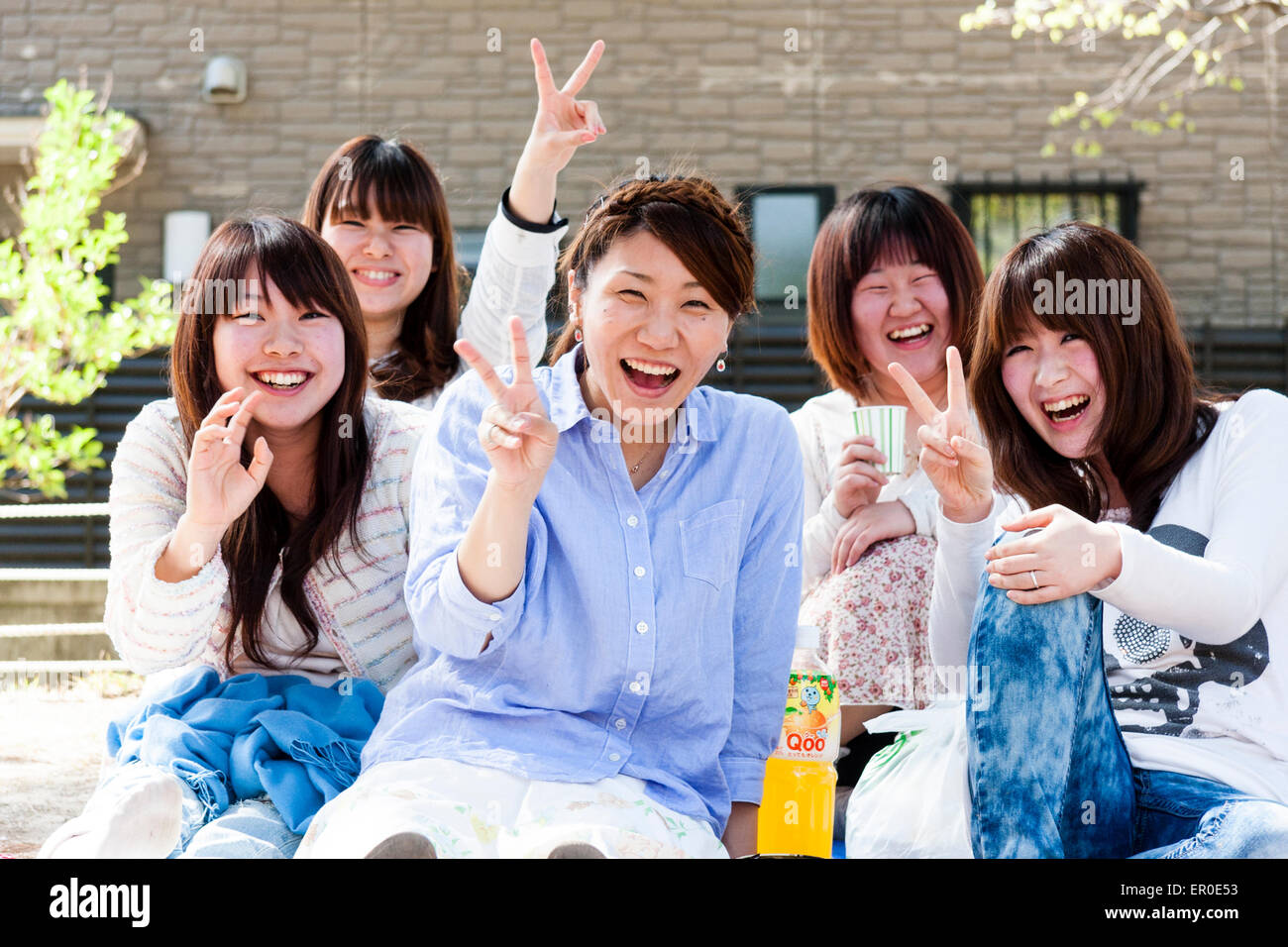 Group Of Young Japanese Women Sitting On Ground During Cherry Blossom
