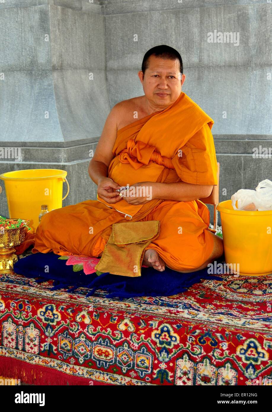 Bangkok, Thailand: An orange robed monk seated on a colourful carpet at ...