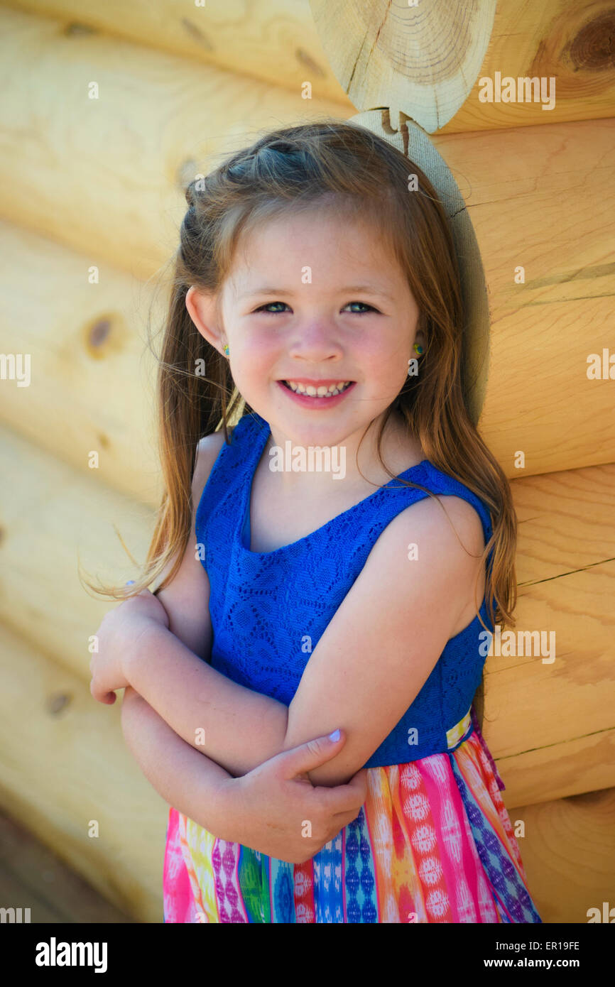 Pretty 4 year old girl in colorful blue dress on log cabin Stock Photo ...