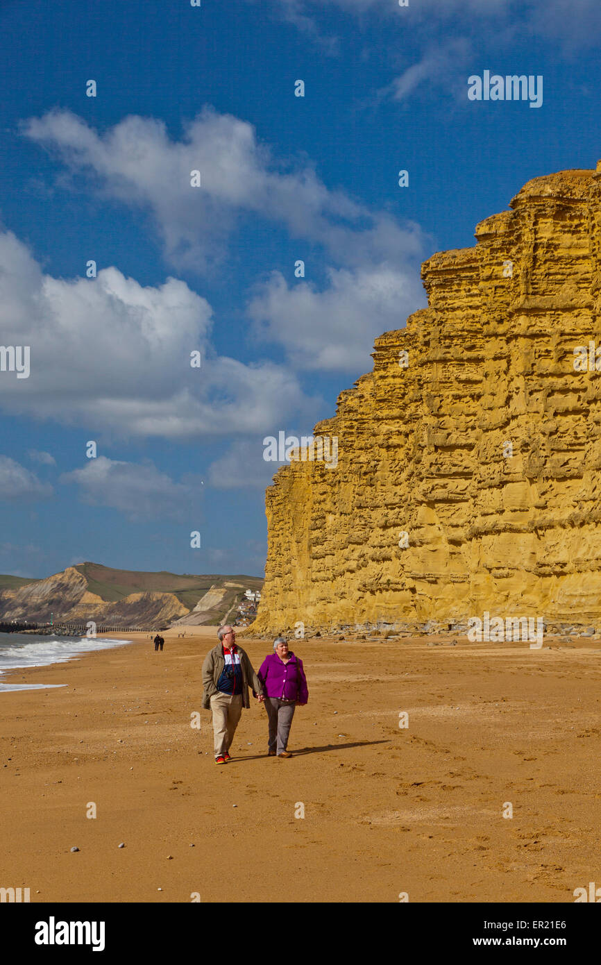 Walkers on the beach below the distinctive banded sandstone strata of ...