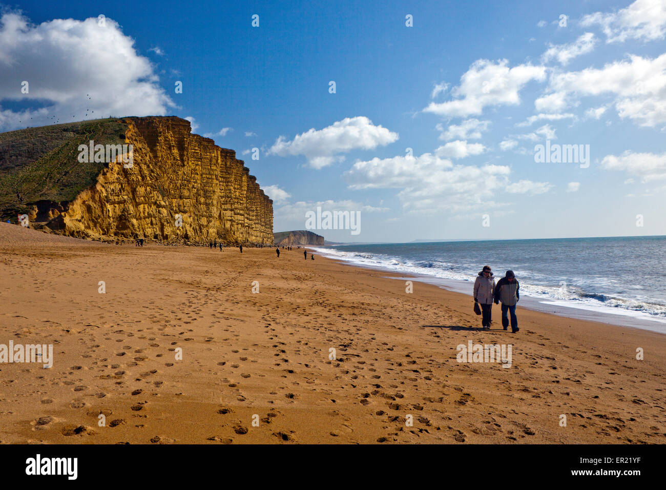 Walkers on the beach below the distinctive banded sandstone strata of ...