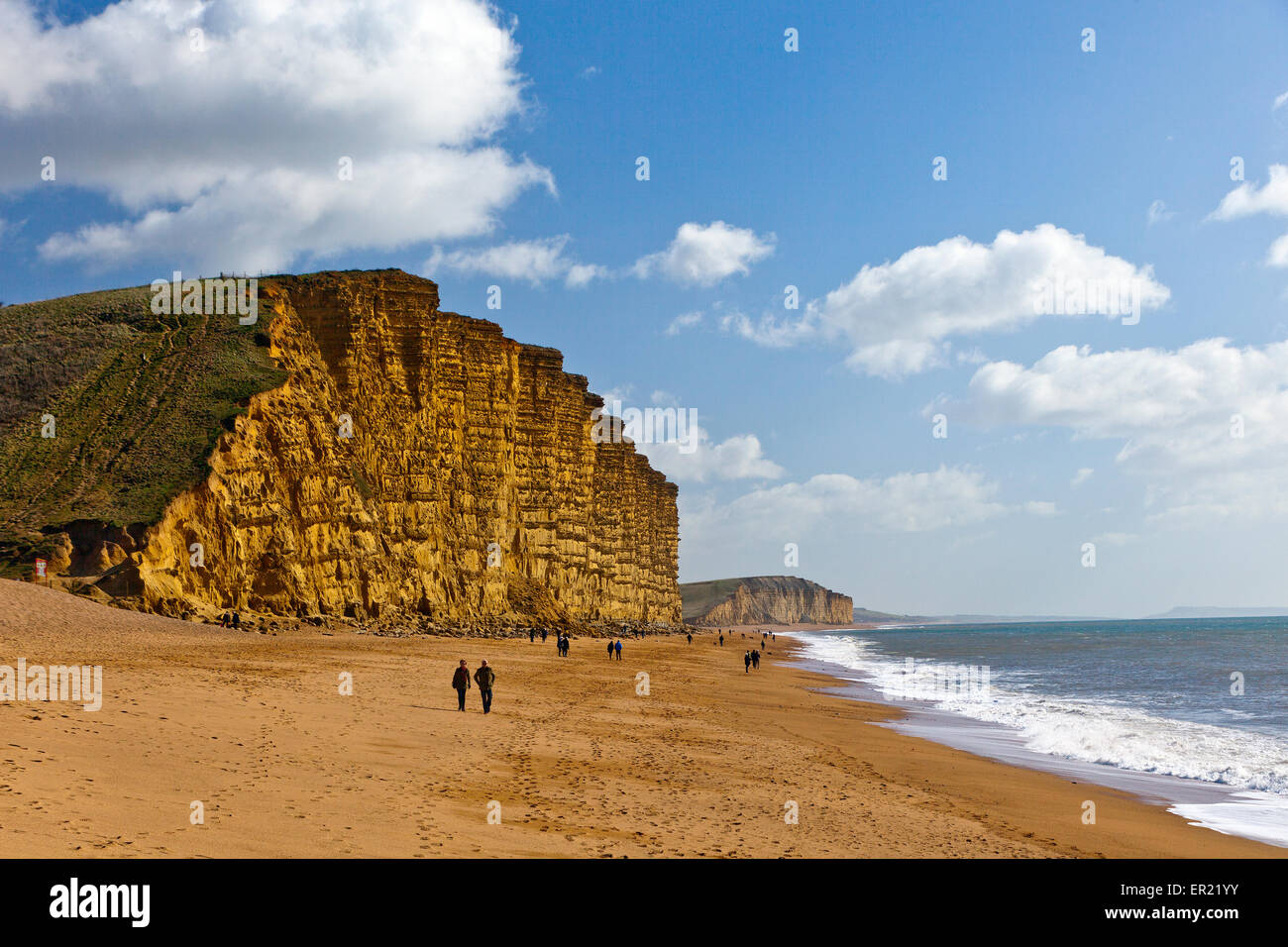 Walkers on the beach below the distinctive banded sandstone strata of ...