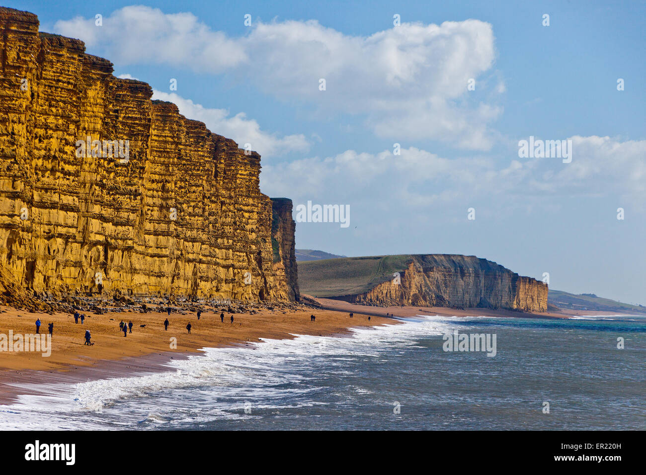 Walkers on the beach below the distinctive banded sandstone strata of ...