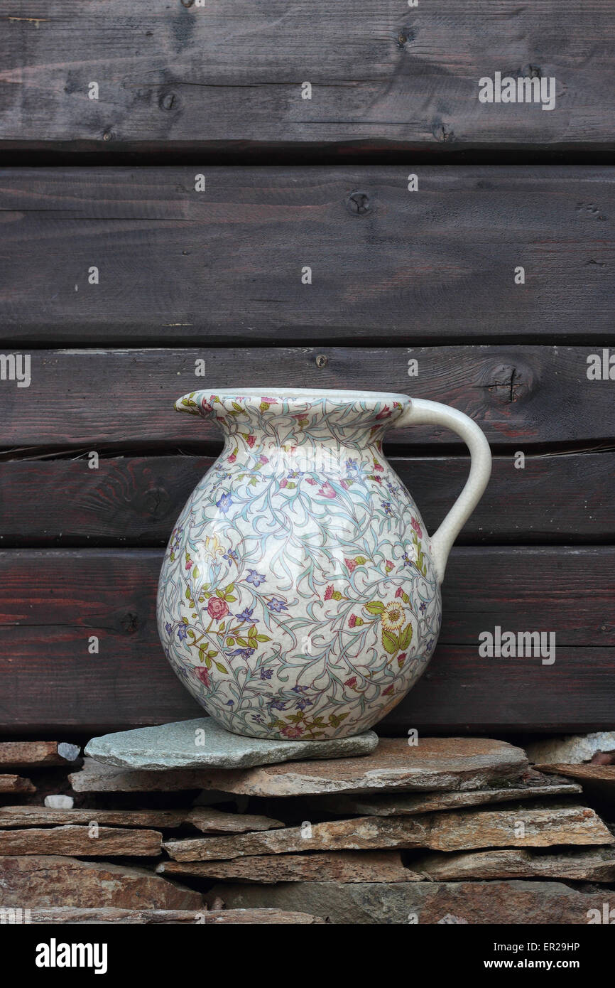 The antique jug with a pattern of flowers lies on brown wood under a ...