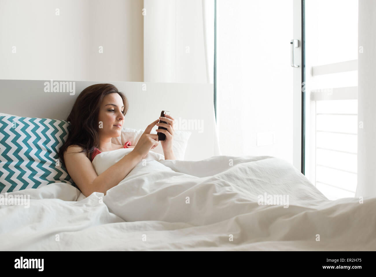 Woman in bed checking social apps with smartphone Stock Photo - Alamy