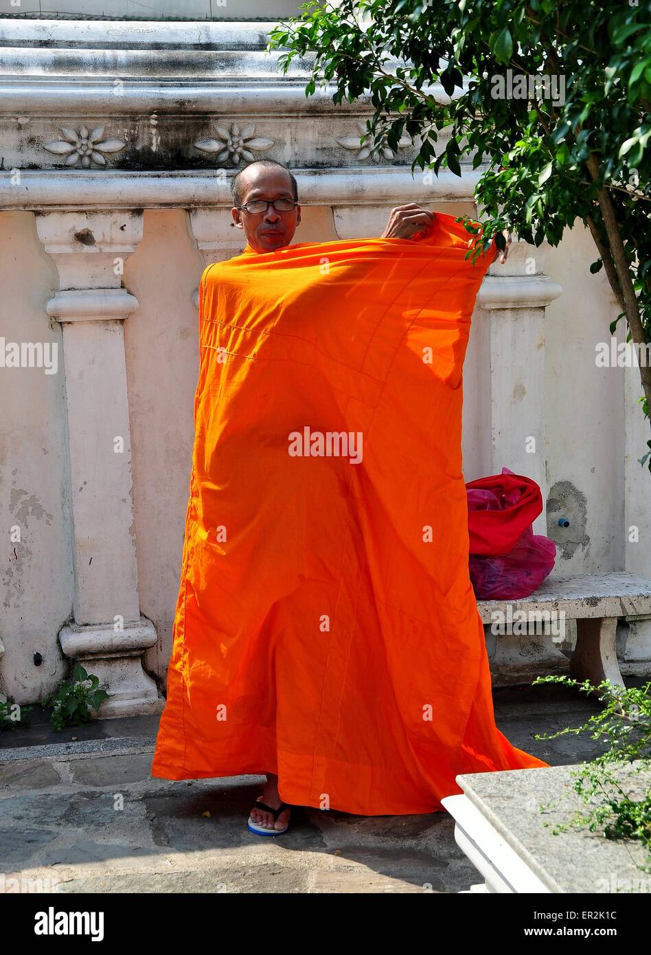 Bangkok, Thailand: Buddhist monk wrapoing an orange robe around his ...