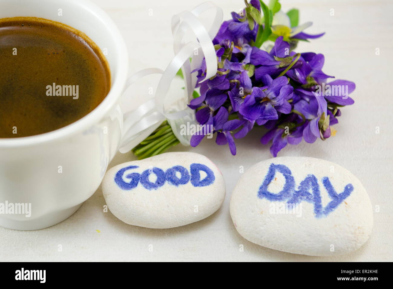 White cup of coffee with flowers and rocks saying "Good day Stock Photo ...