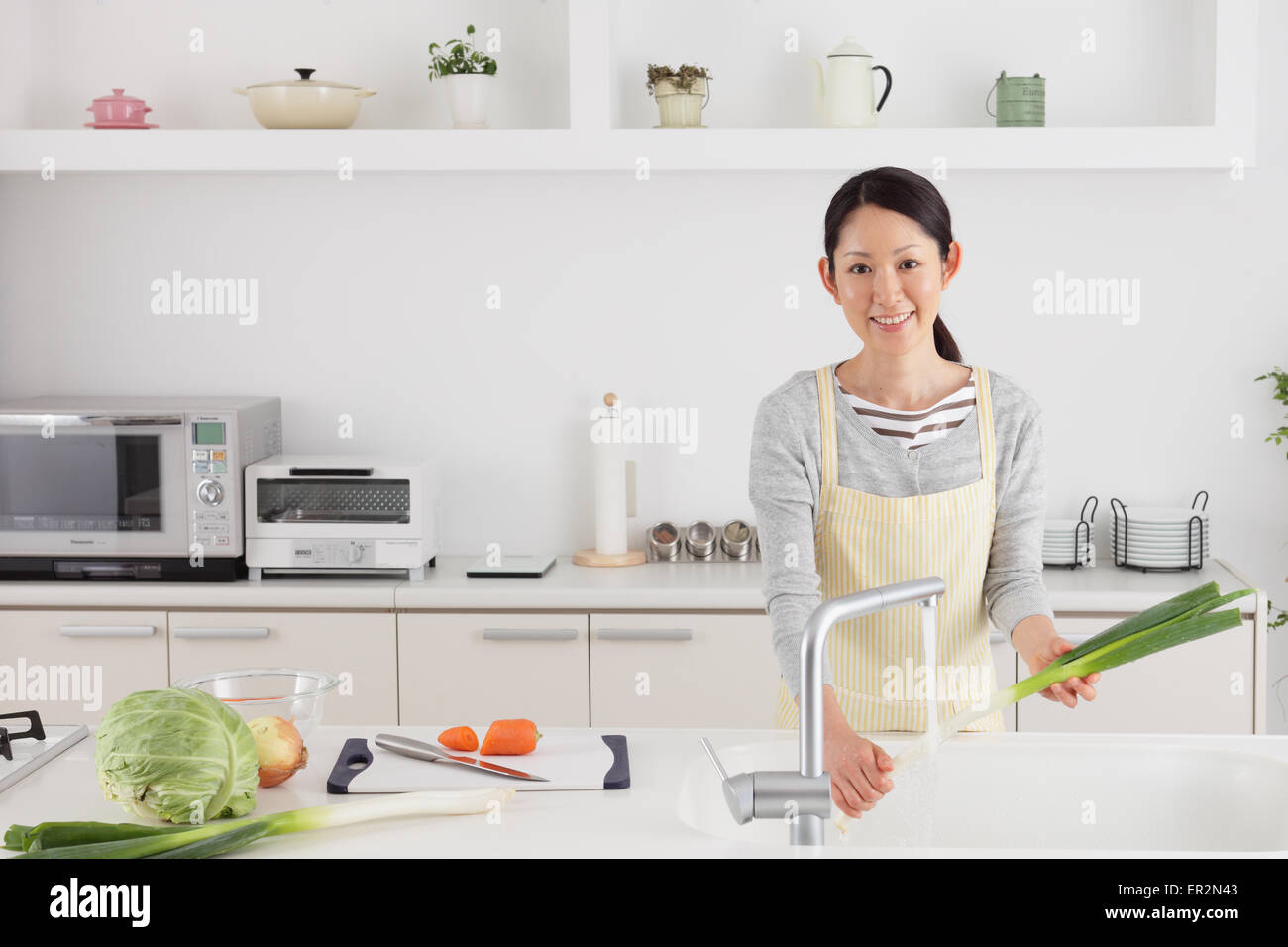 Woman washing green onions in an open kitchen Stock Photo - Alamy