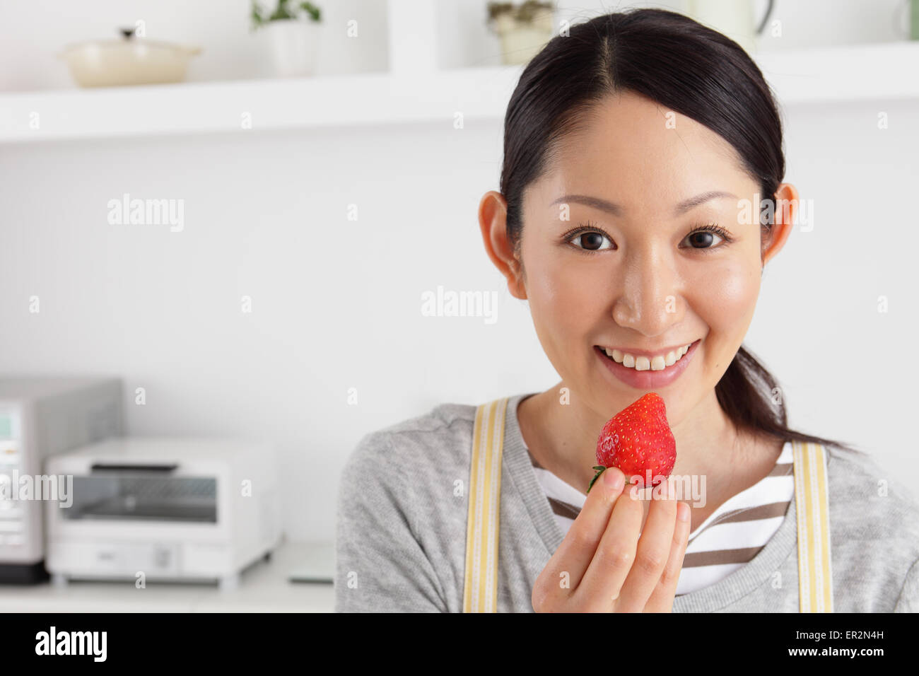 Woman eating strawberry in an open kitchen Stock Photo - Alamy