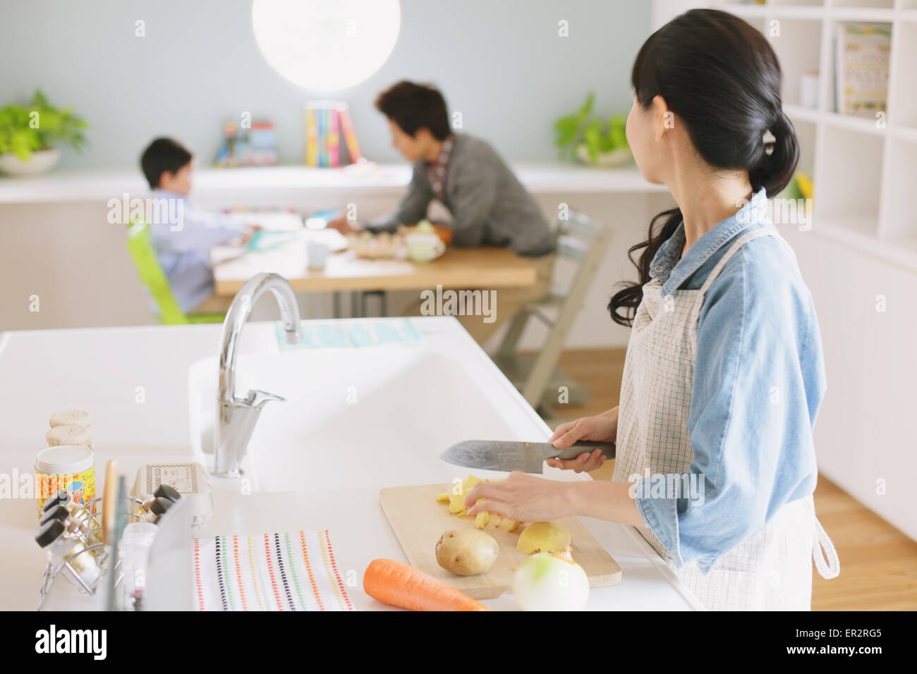 Mother cooking in an open kitchen watching father and son doing ...