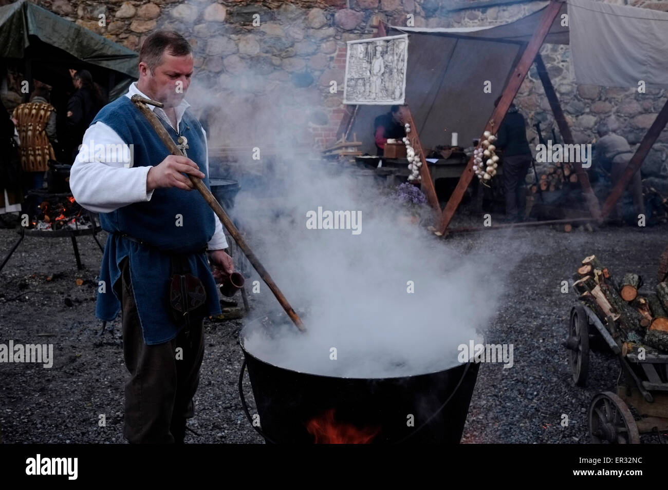 Man in traditional medieval outfit stirs soup in large cauldron pot ...