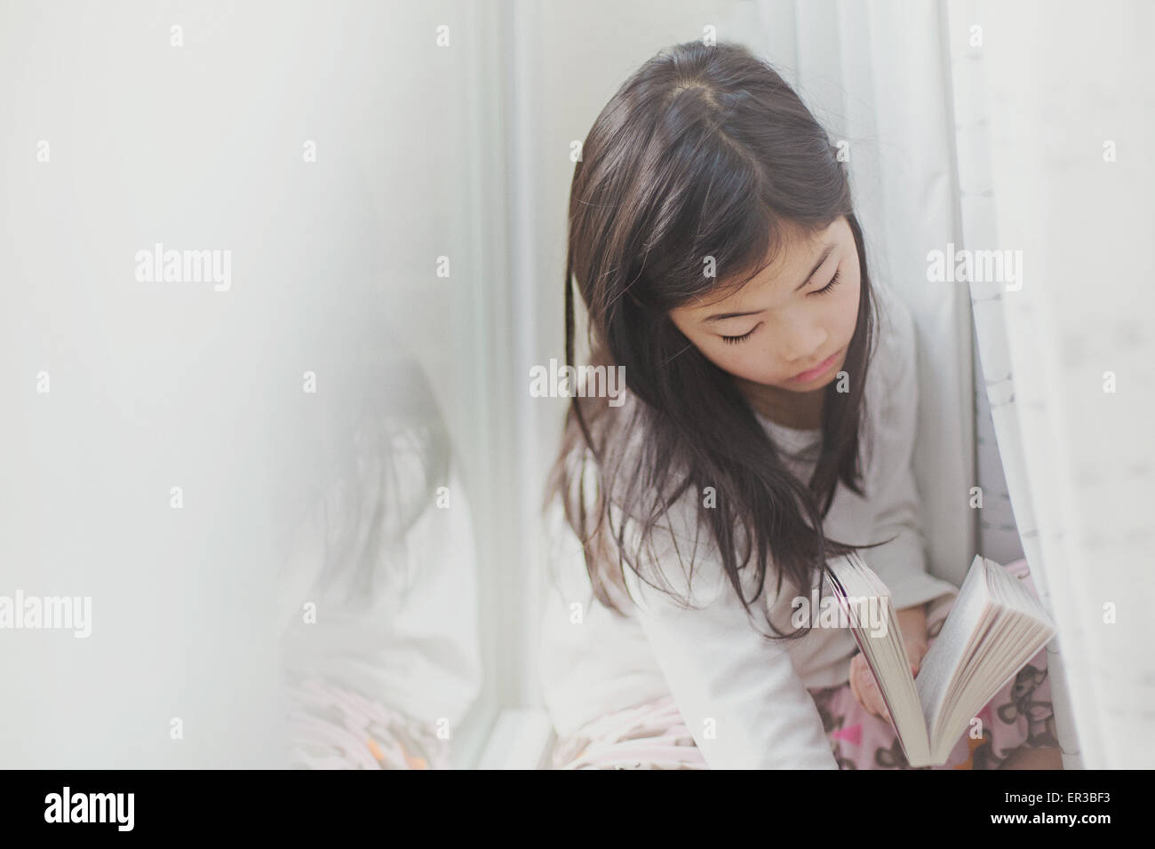 Girl sitting on a window sill reading a book Stock Photo - Alamy