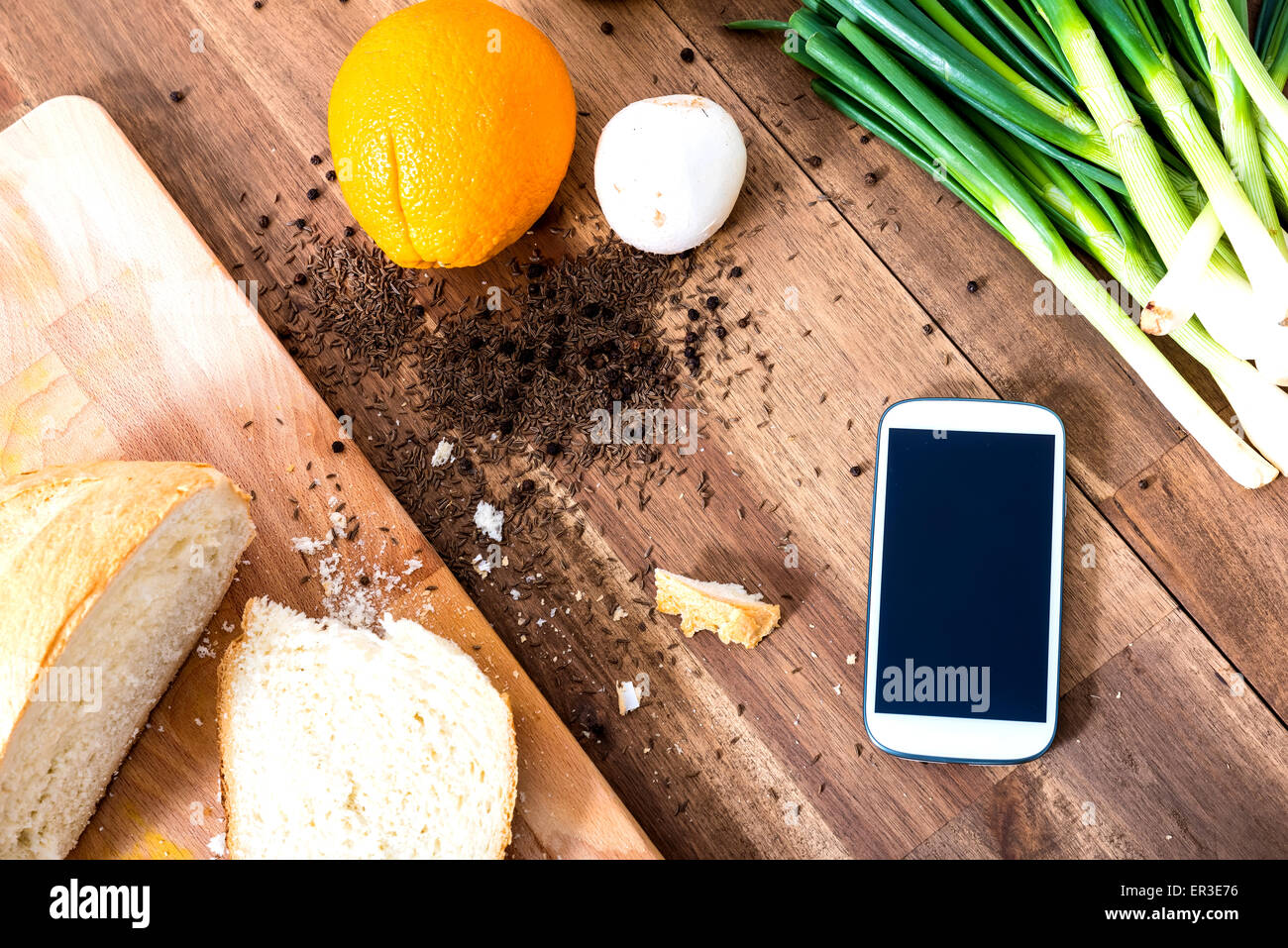 A smartphone lying in a natural kitchen with white bread, spices ...