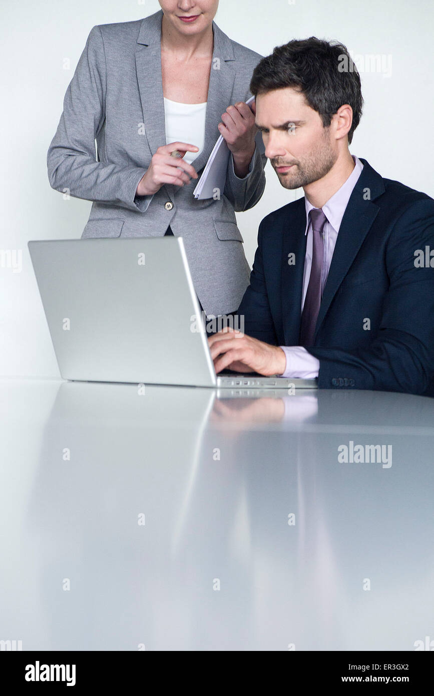 Businessman working on laptop computer, colleague looking over his ...