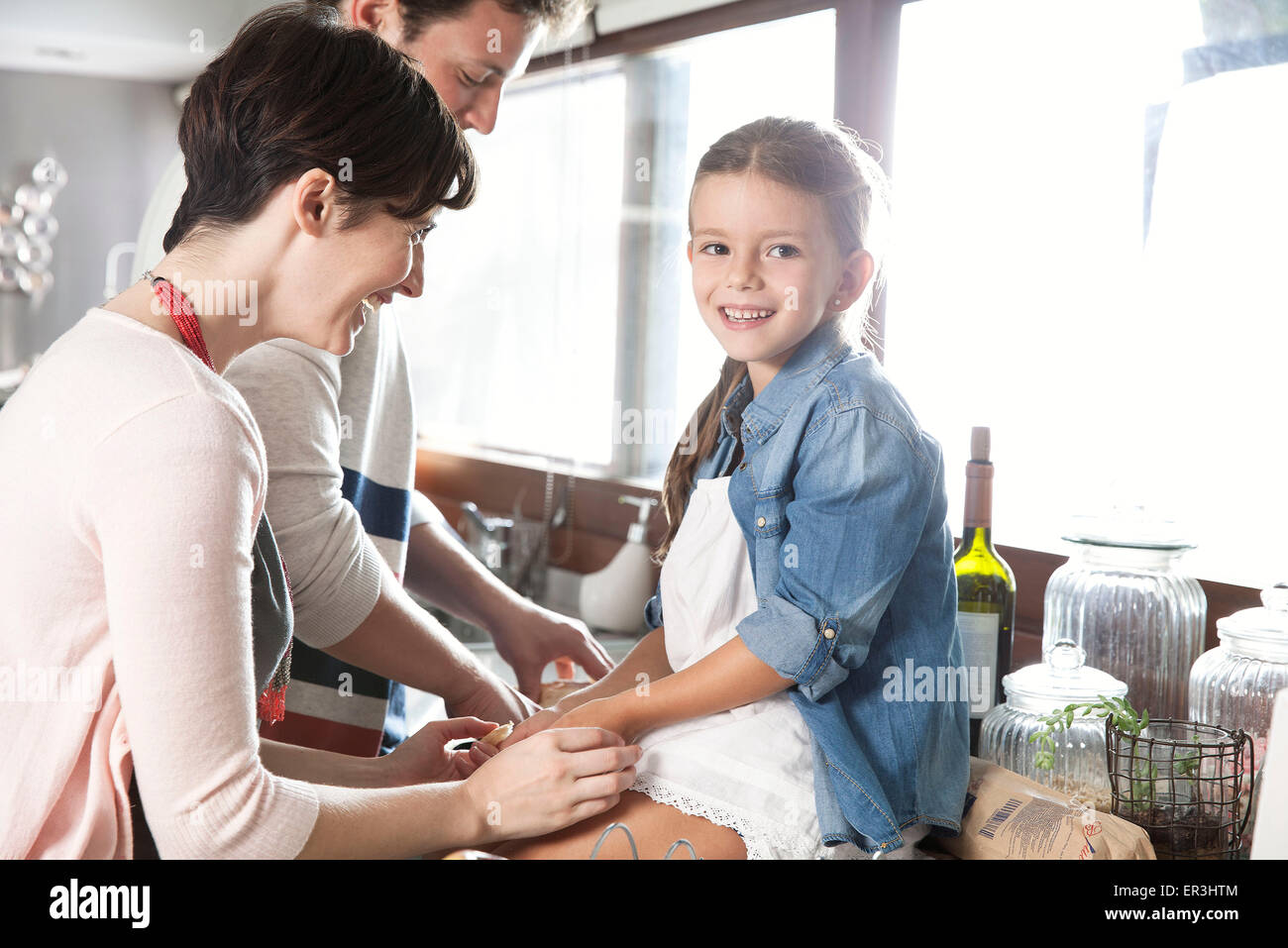 Family spending time together in kitchen, girl sitting on counter ...