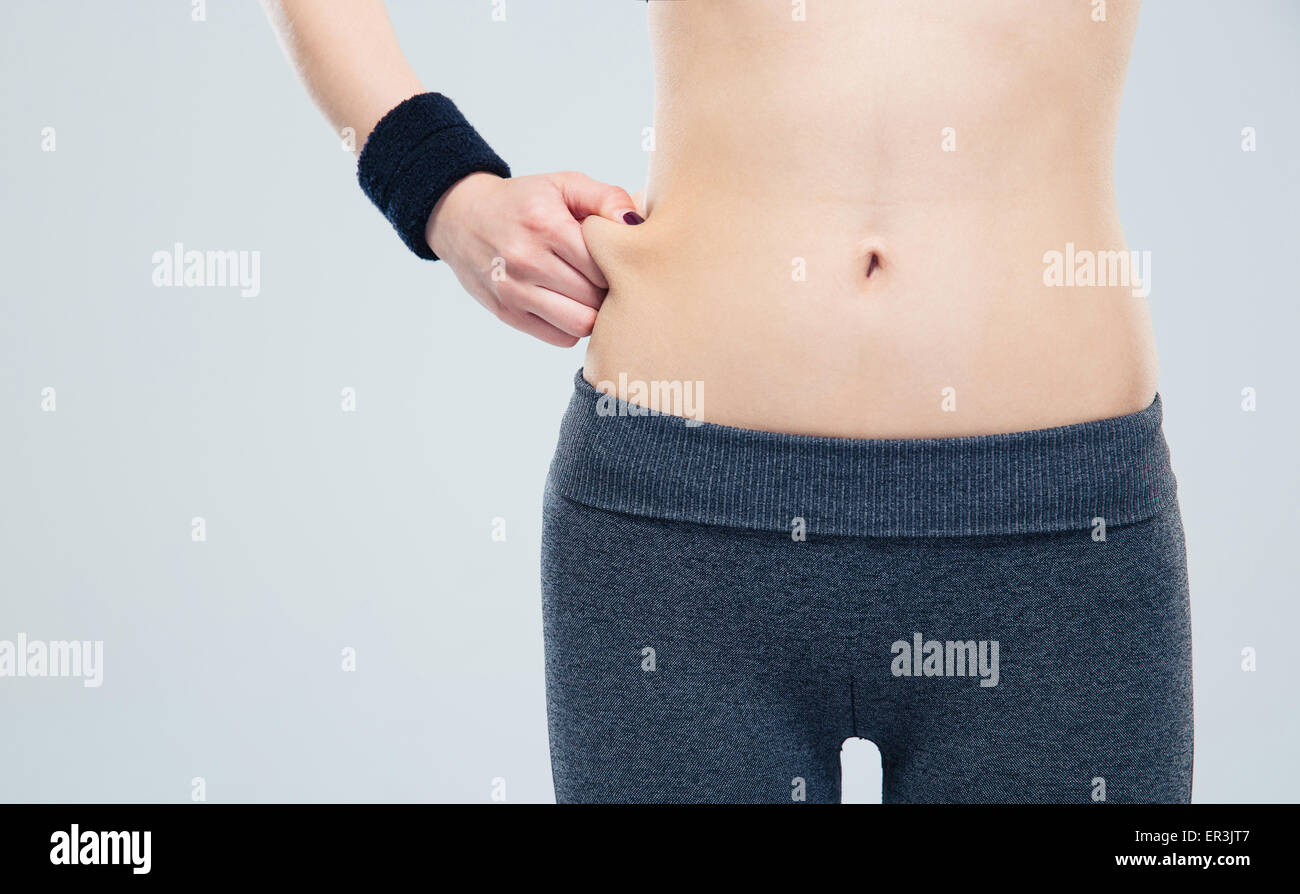 Closeup portrait of a sporty woman pinch a fat on her abdomen over gray ...