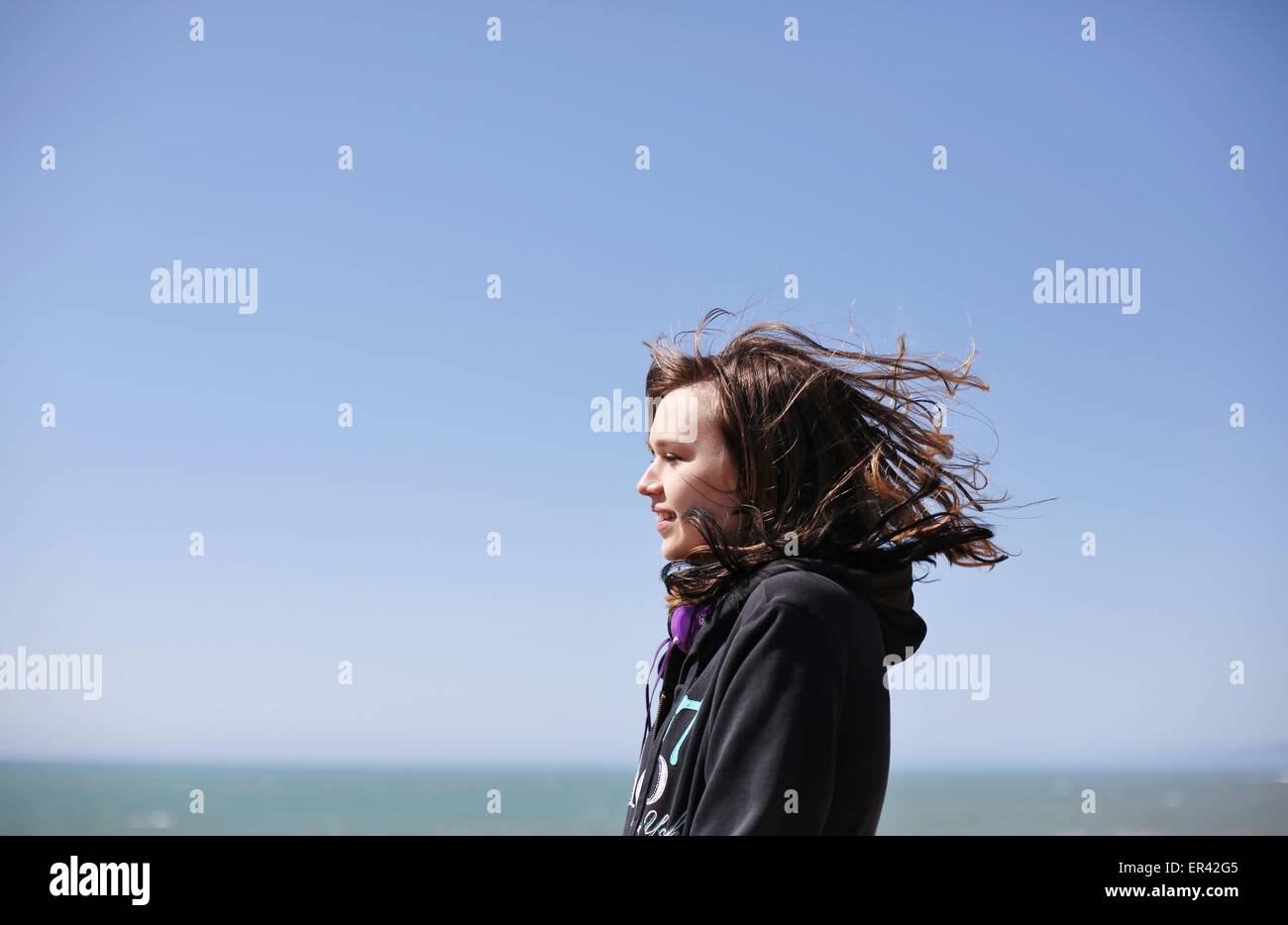 A girl standing next to the ocean with wind whipped hair Stock Photo ...