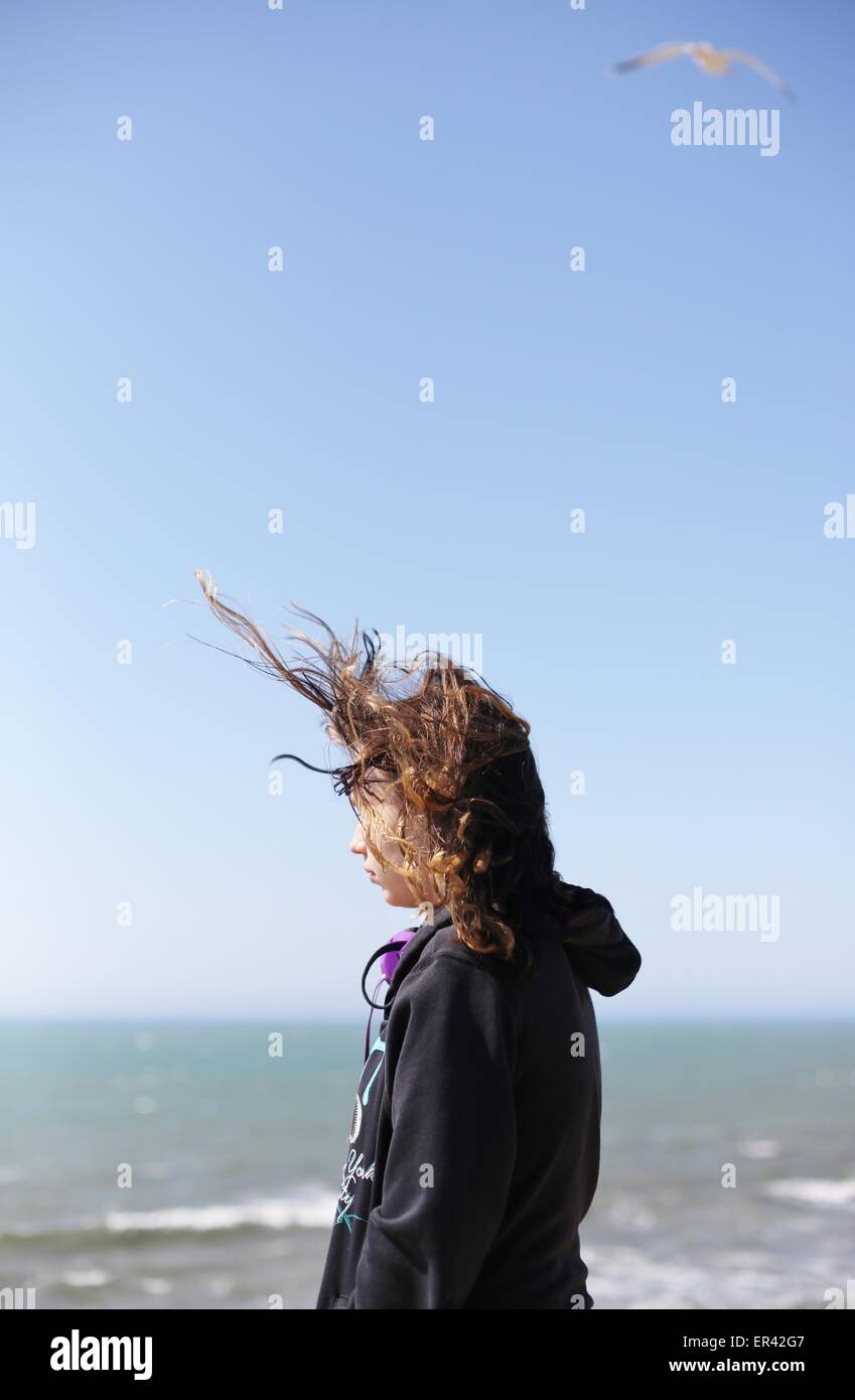 A girl standing next to the ocean with wind whipped hair Stock Photo ...