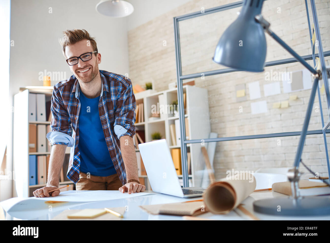 Happy young employee standing by workplace in office Stock Photo - Alamy