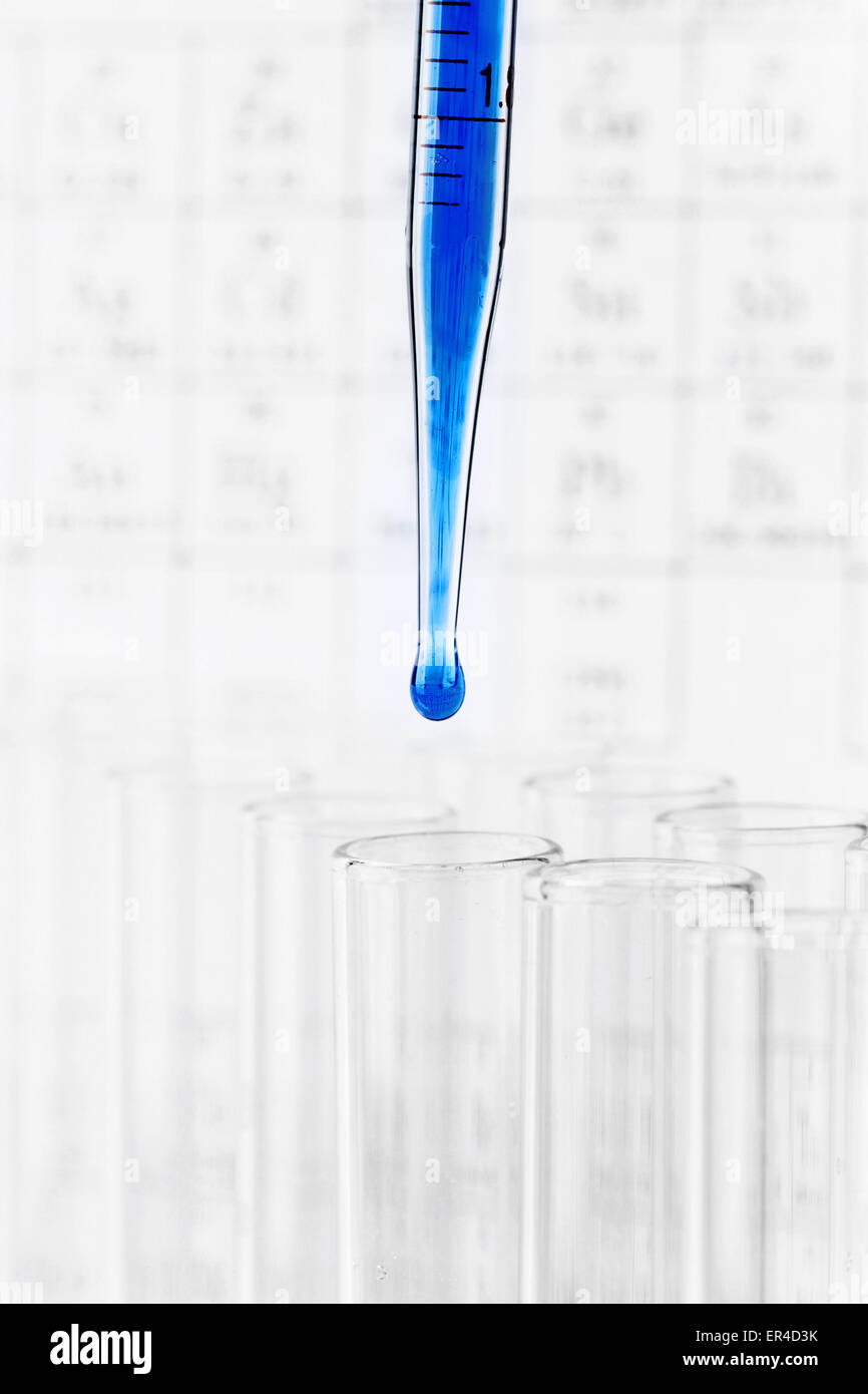 Laboratory pipette with drop of liquid over glass test tubes in a ...