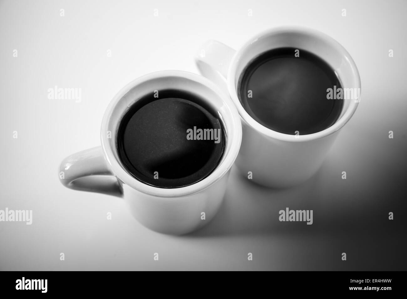 Two cups full of coffee stand on a table with black shadow, monochrome ...