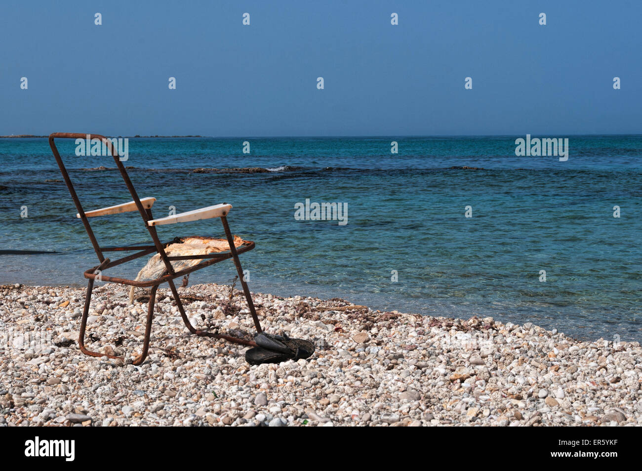 Old rusty ramshackle beach chair standing on sea pebbles on the shore ...