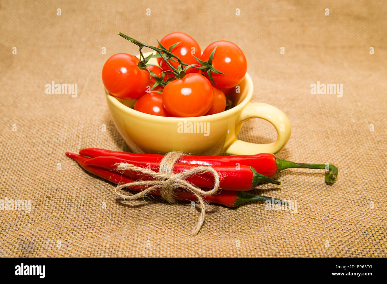 Cherry tomatoes in a yellow cup and Chile peppers tied with a rope on ...