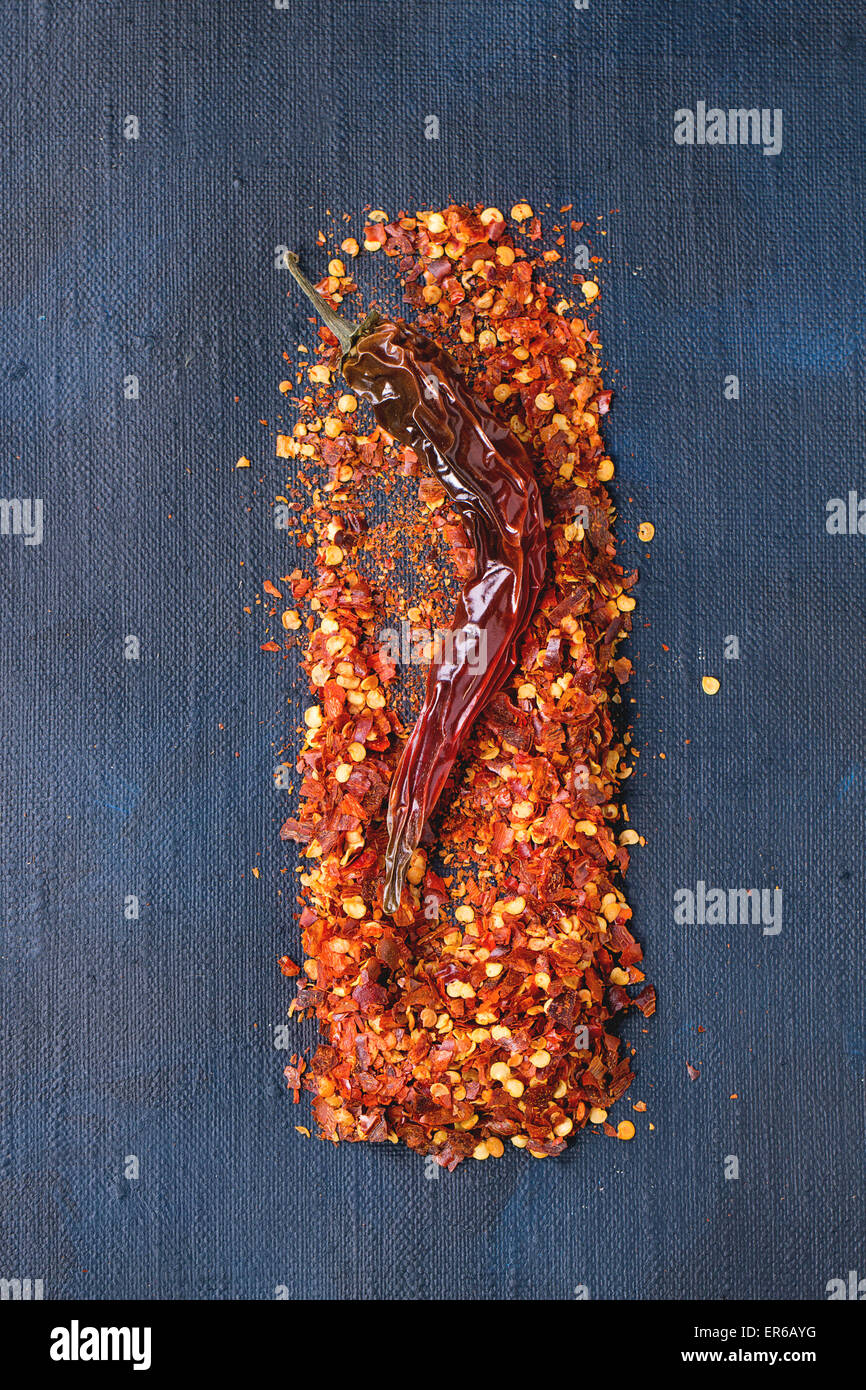 Flakes of red hot chili peppers and one dryed chili pepper over dark ...