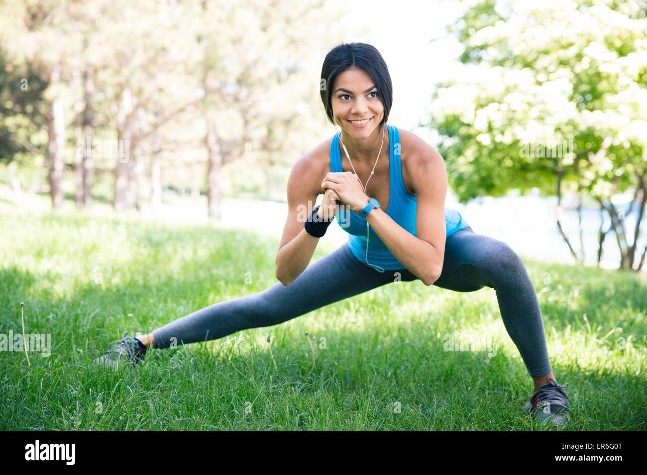 Smiling sporty woman doing stretching exercise outdoors in park ...