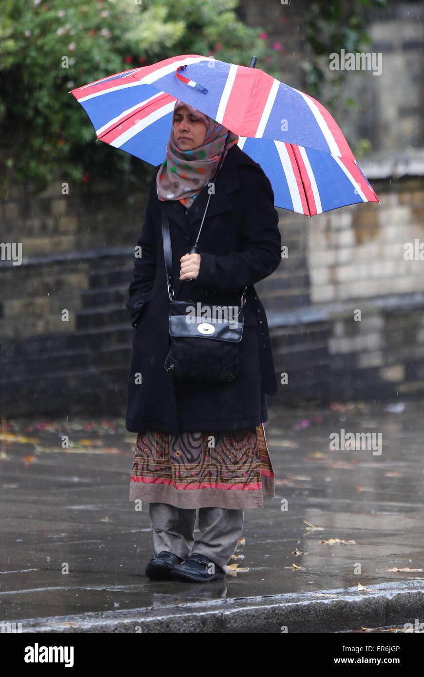 A woman shelters from torrential rain under a Union Jack umbrella ...