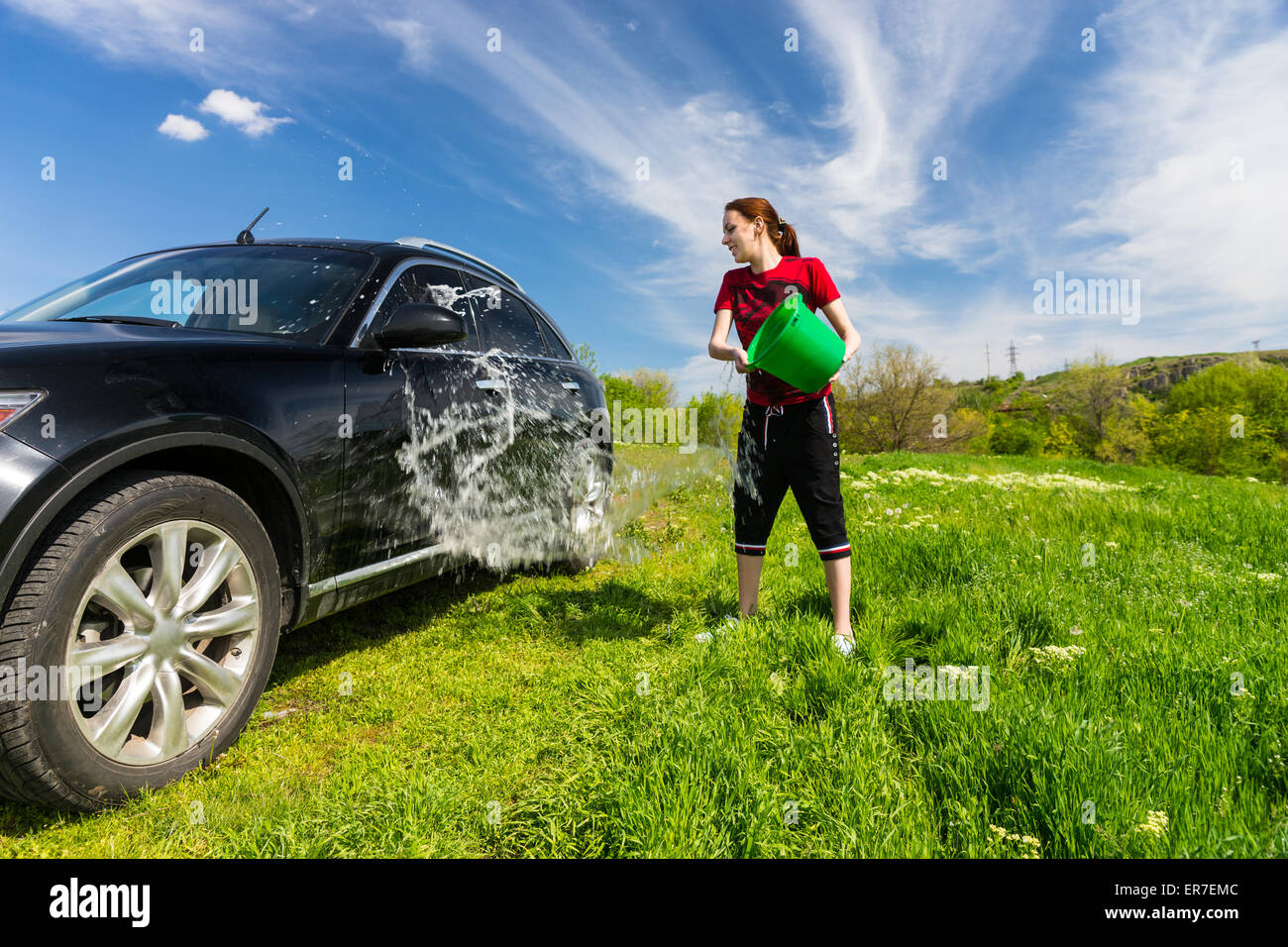 Young Woman Washing Black Luxury Vehicle in Grassy Green Field on ...