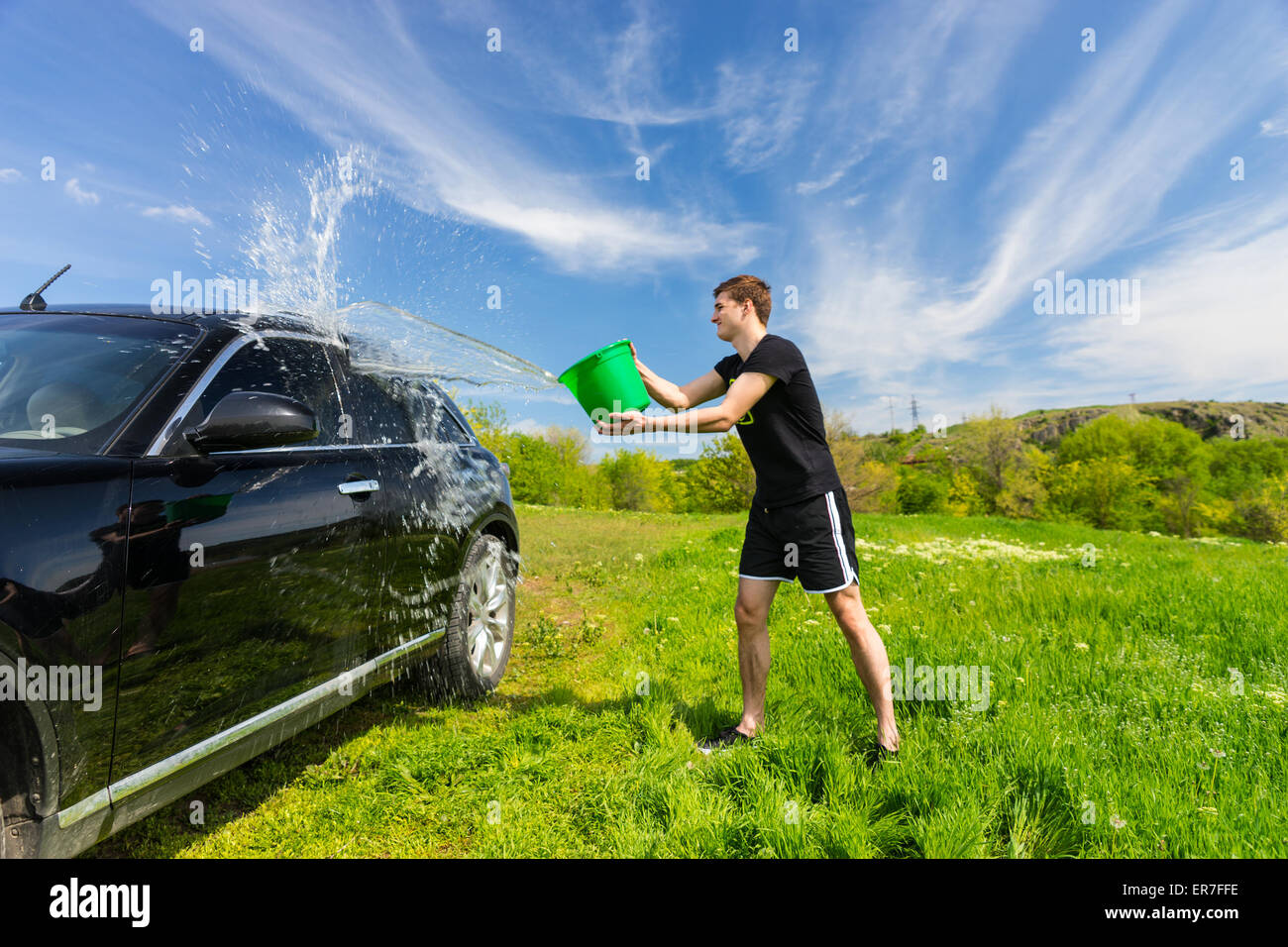 Young Man Washing Black Luxury Vehicle in Grassy Green Field on Bright ...