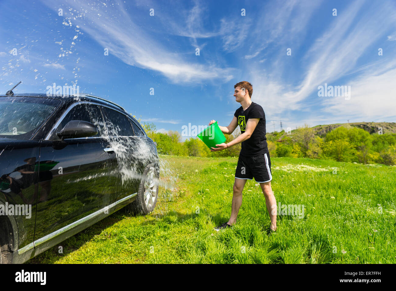 Young Man Washing Black Luxury Vehicle in Grassy Green Field on Bright ...