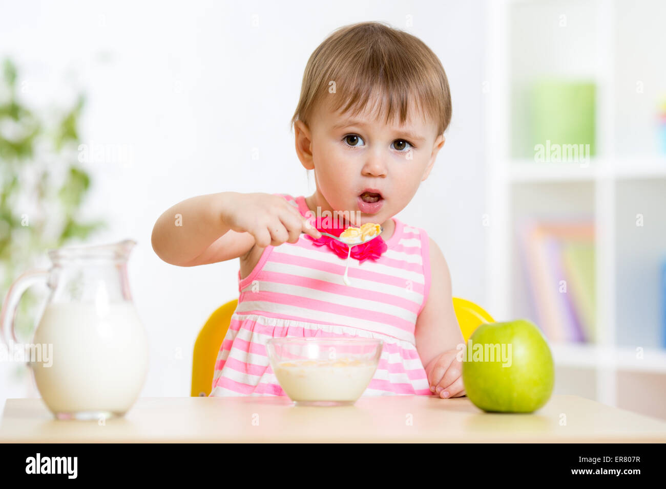 Little girl eating cornflakes with milk at table in home Stock Photo ...