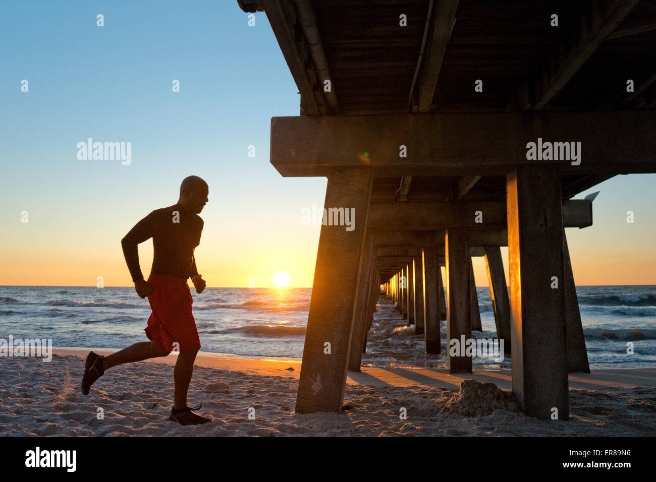 Man running under a pier on the beach at sunset Stock Photo - Alamy