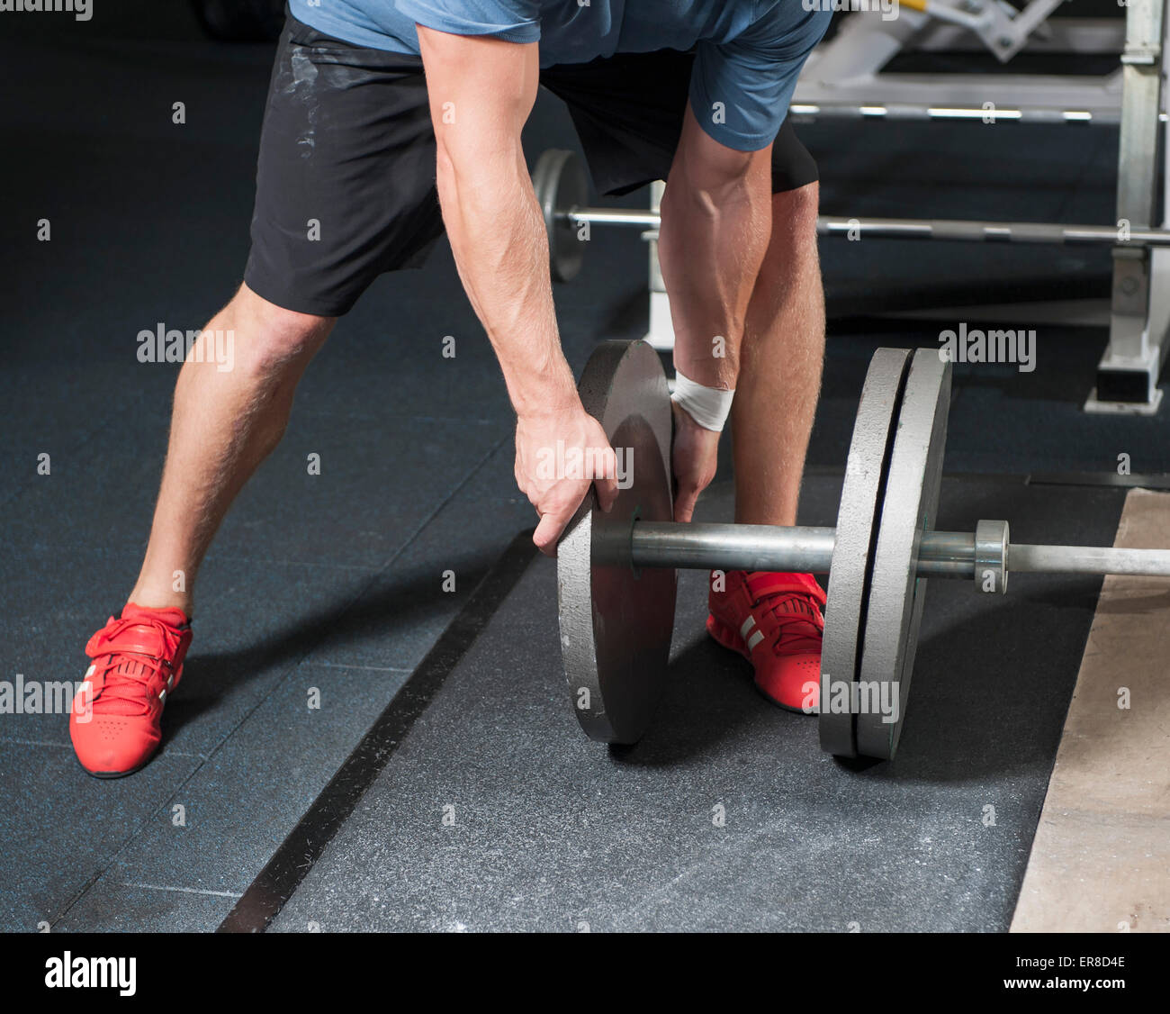 Low section of man adding weights on barbell Stock Photo - Alamy