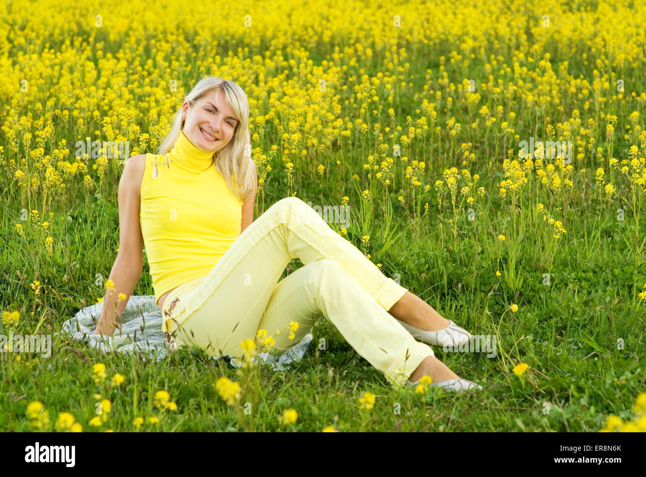 Beautiful young woman sitting in a flower field Stock Photo - Alamy