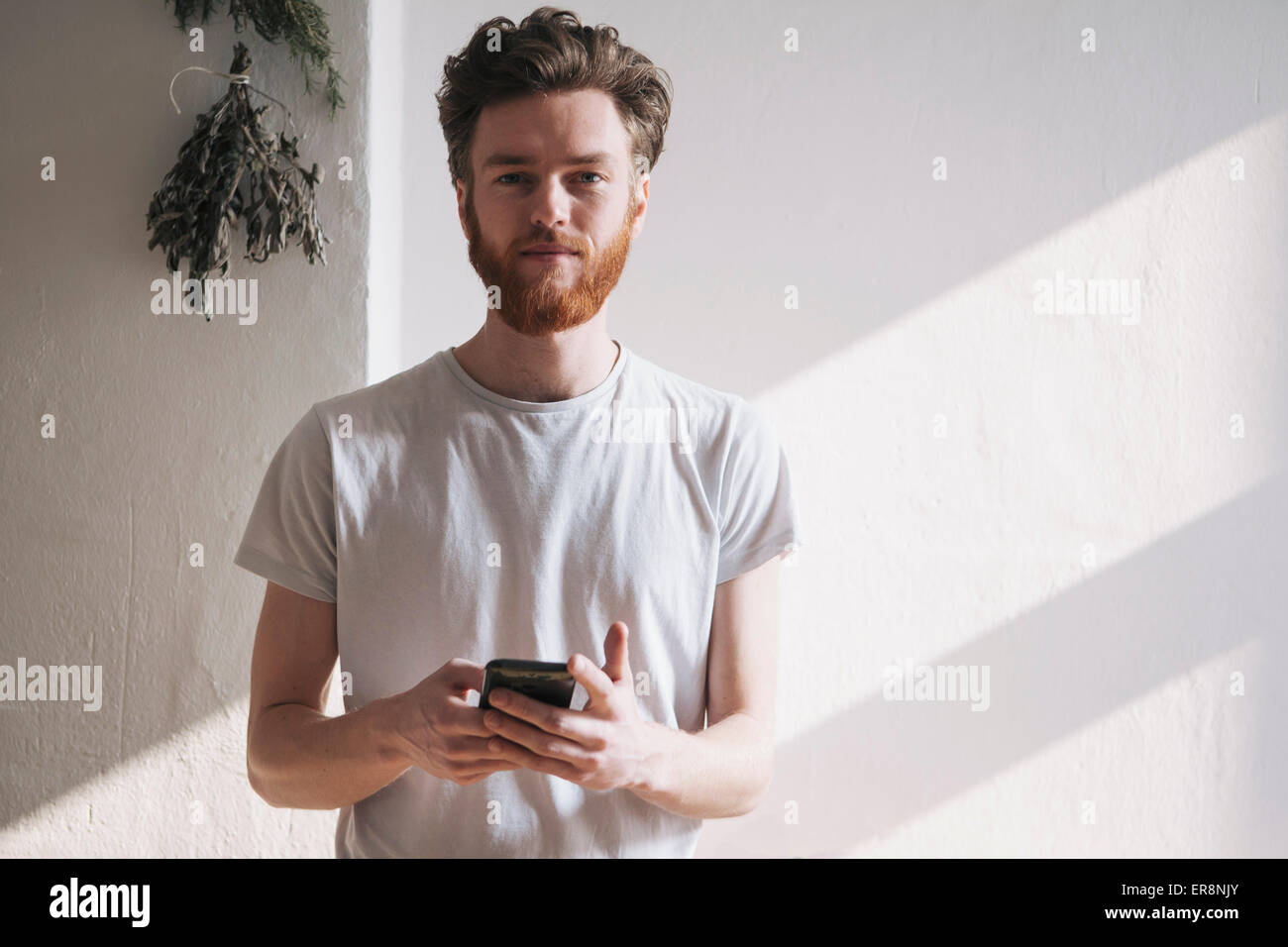 Portrait of confident young man holding mobile phone at home Stock Photo - Alamy
