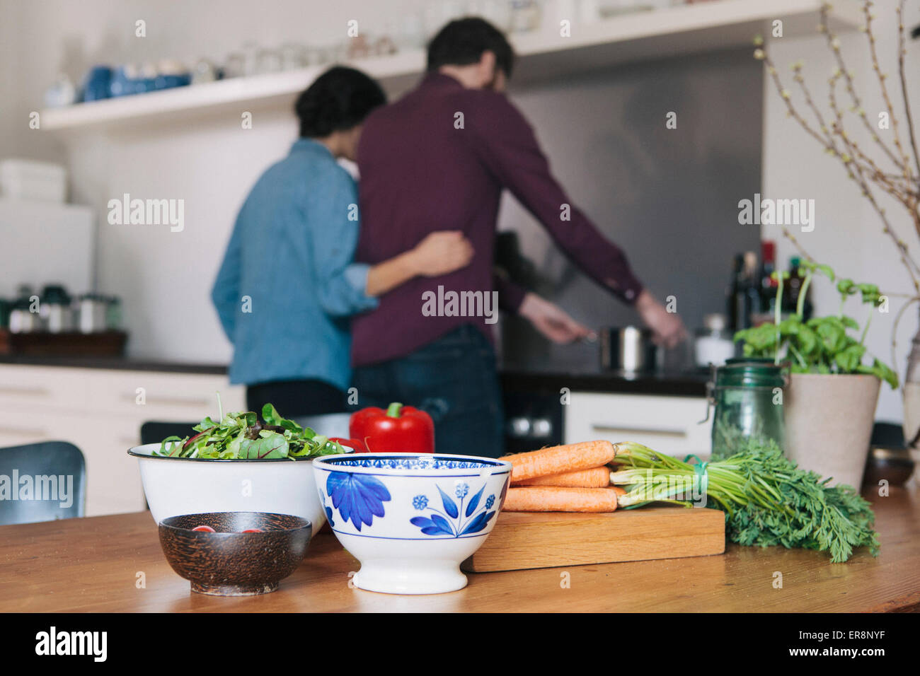 Vegetables on kitchen table with couple cooking in background Stock ...